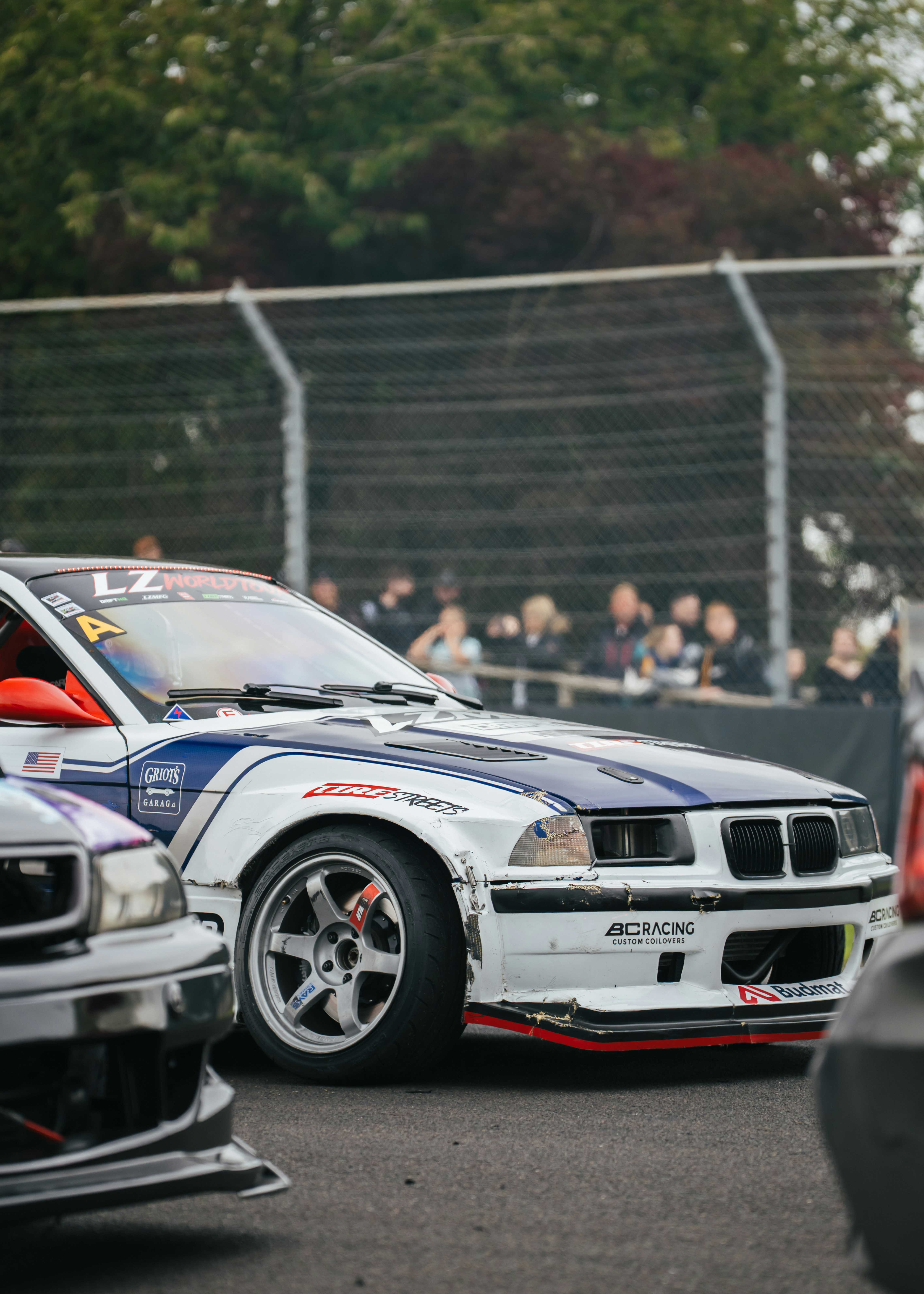 Drifting race cars with spectators in background.