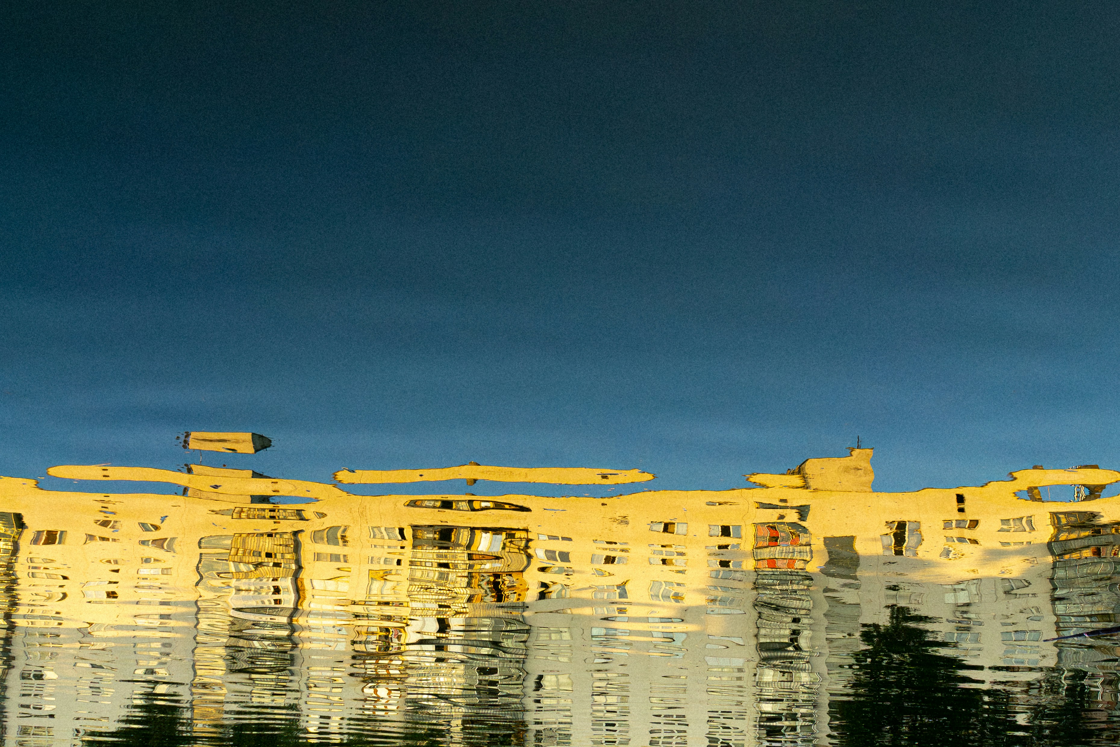 Golden reflections of buildings ripple across the calm surface of water, creating an abstract interplay of light and structure.
