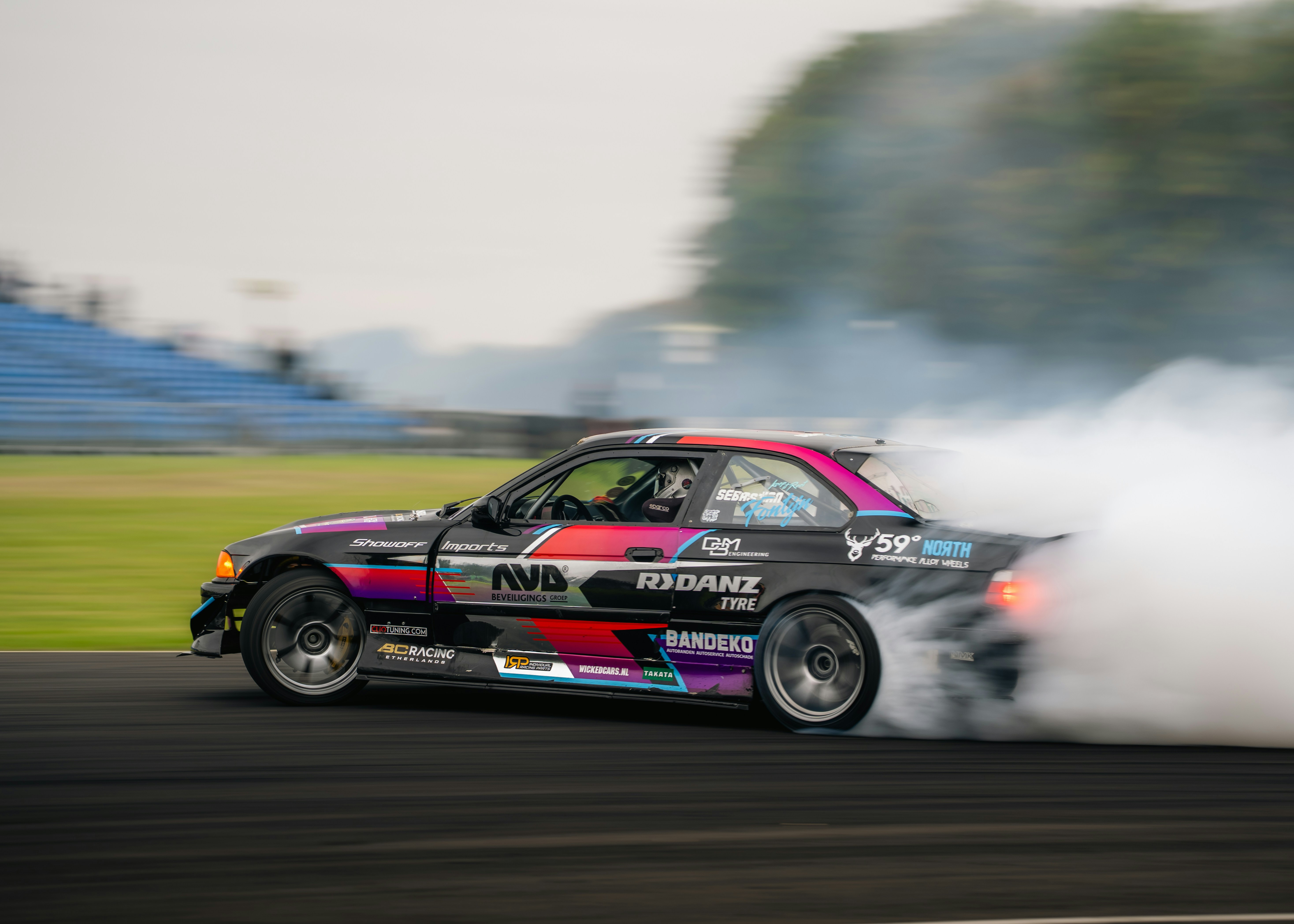 A high-performance car executing a drift, surrounded by billowing smoke on a racetrack. The vibrant colors of the vehicle contrast against the blurred background.