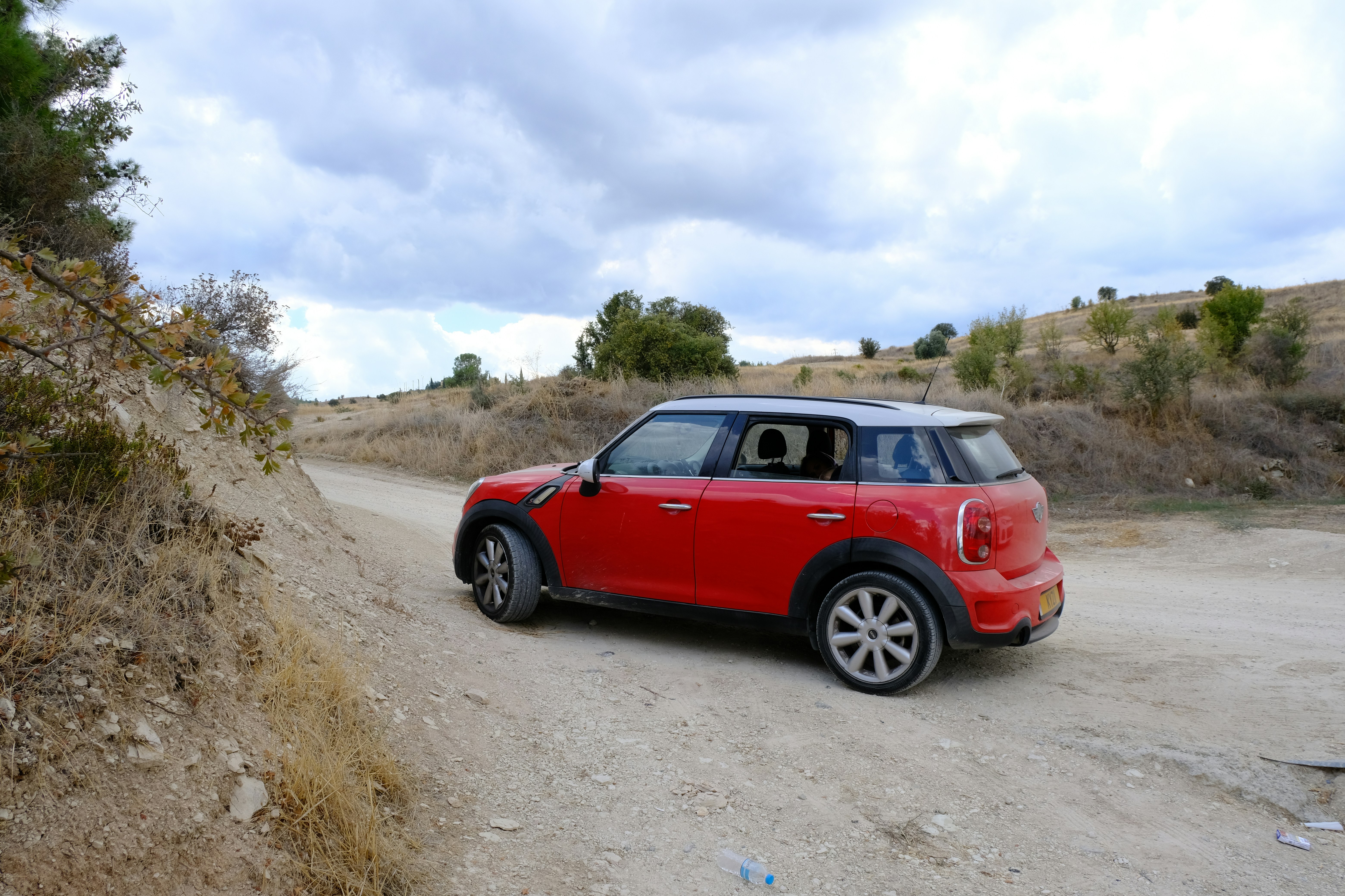 Red compact SUV on a dusty hillside road under a cloudy sky