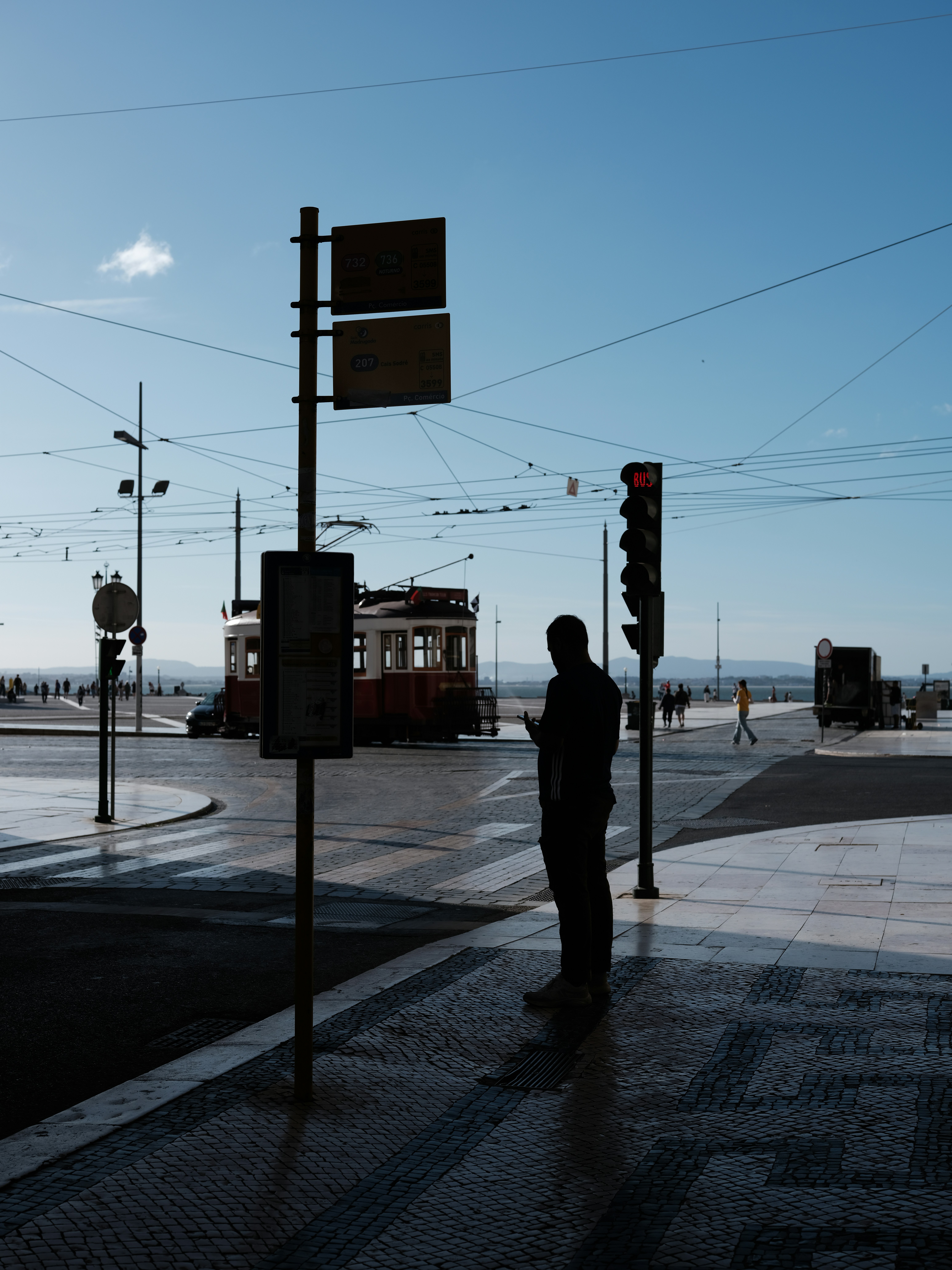 I saw this man standing there in the shadow for a while. It was more than enough time to feel the nervousness of his waiting, phone in hand, not knowing if what he longed for would arrive with the next light. What he could not determine, hope projected. | Silhouette of man at street corner with tram