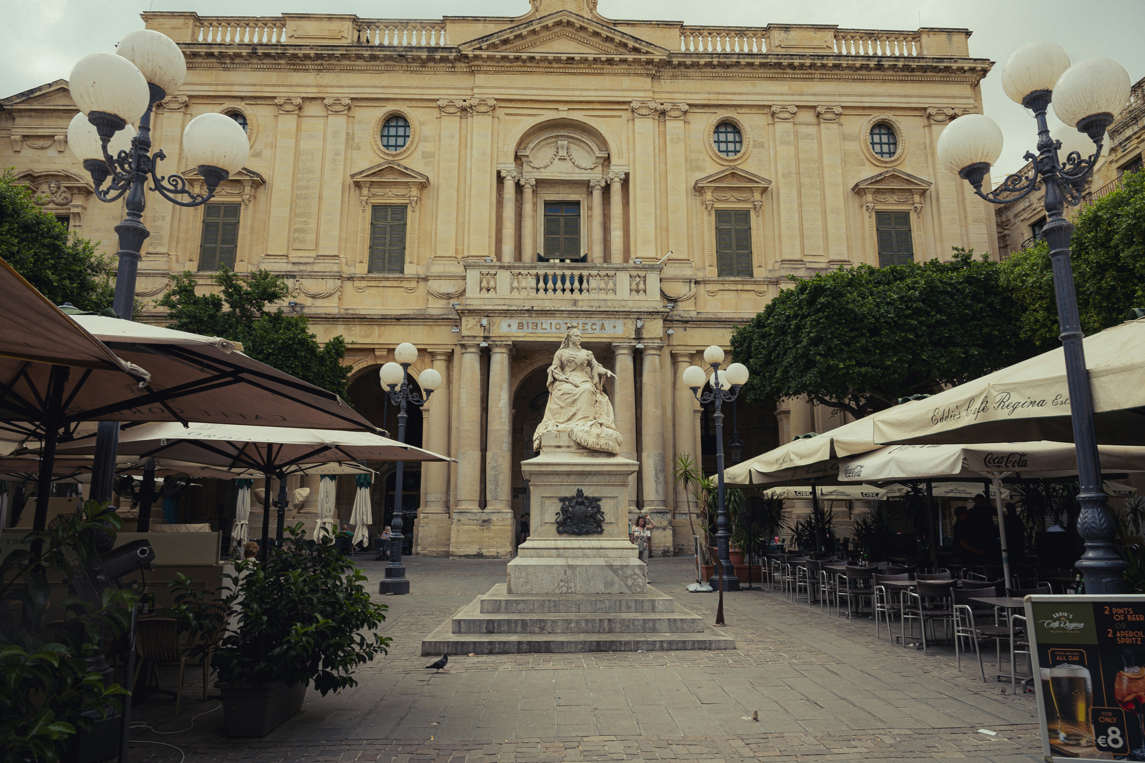 Grand architectural facade with a central statue surrounded by outdoor dining, showcasing a blend of culture and leisure.