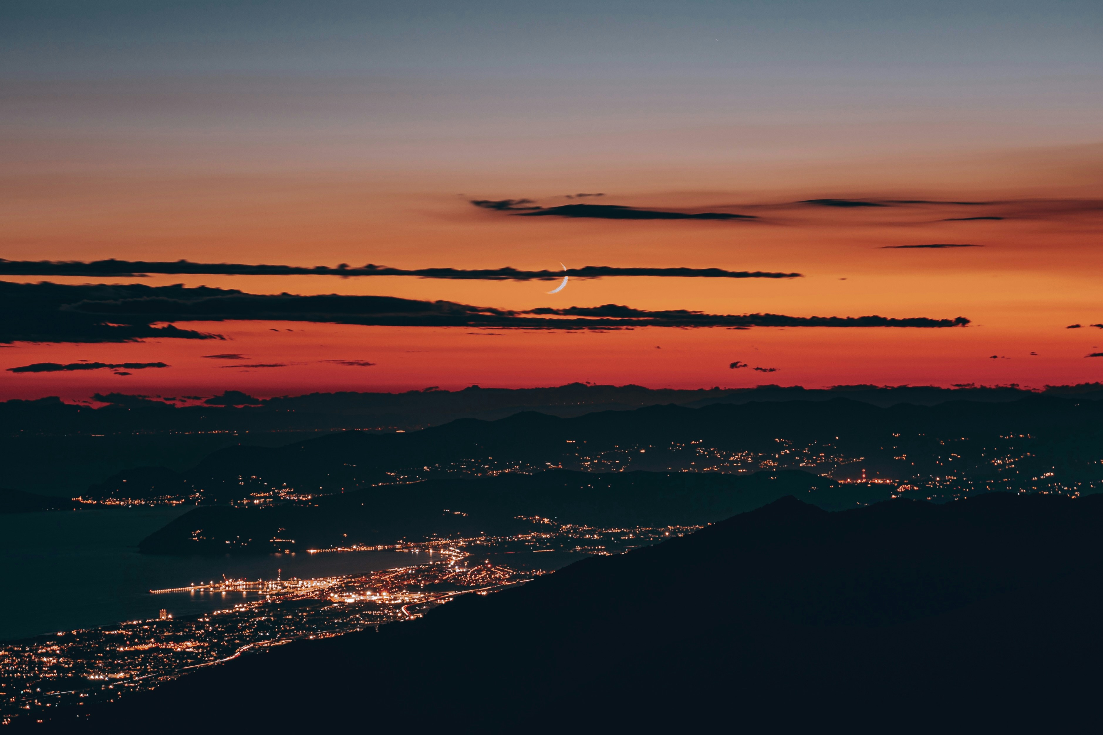 City lights twinkle under a dramatic sunset sky.