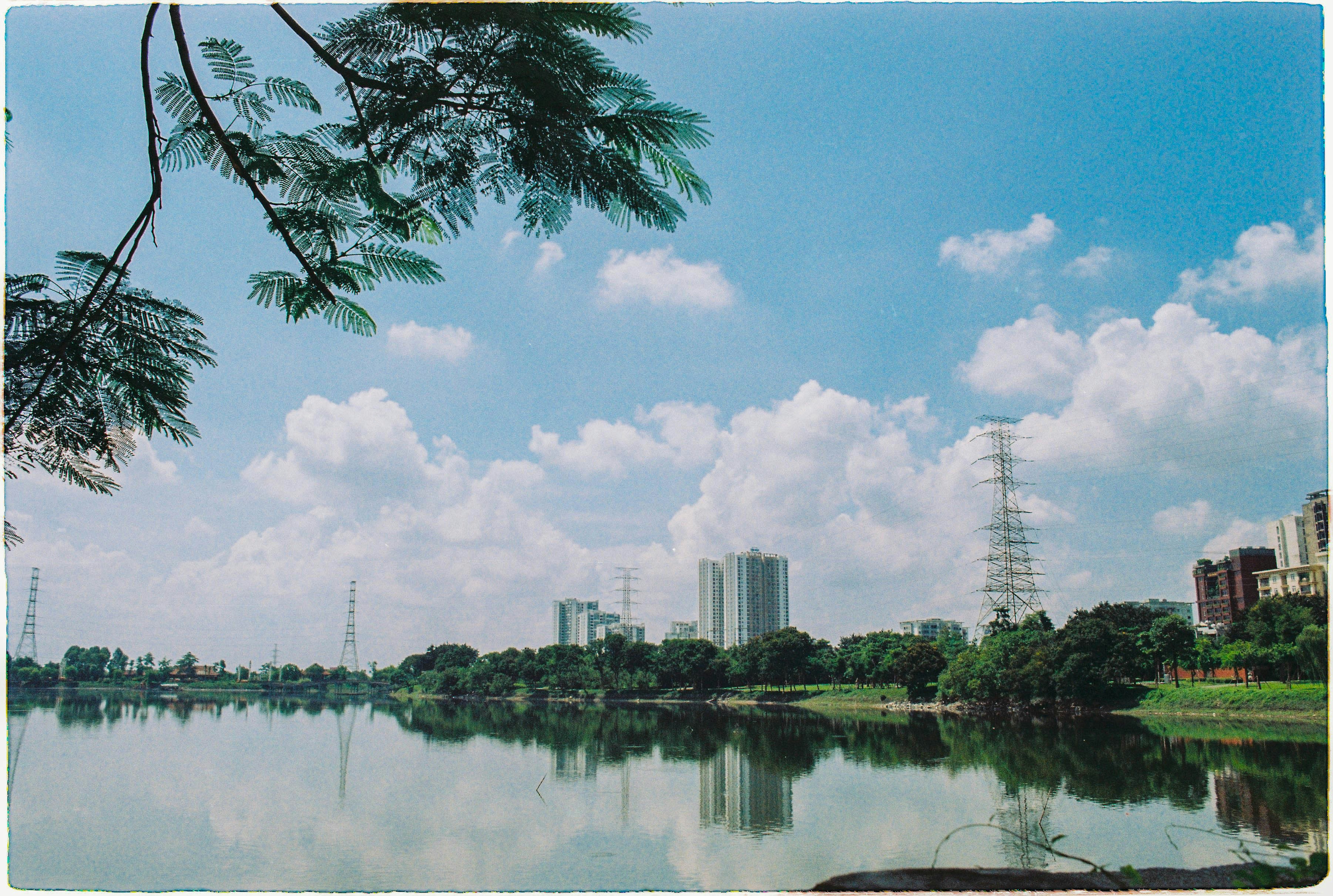 Calm lake reflecting buildings and trees under blue sky.