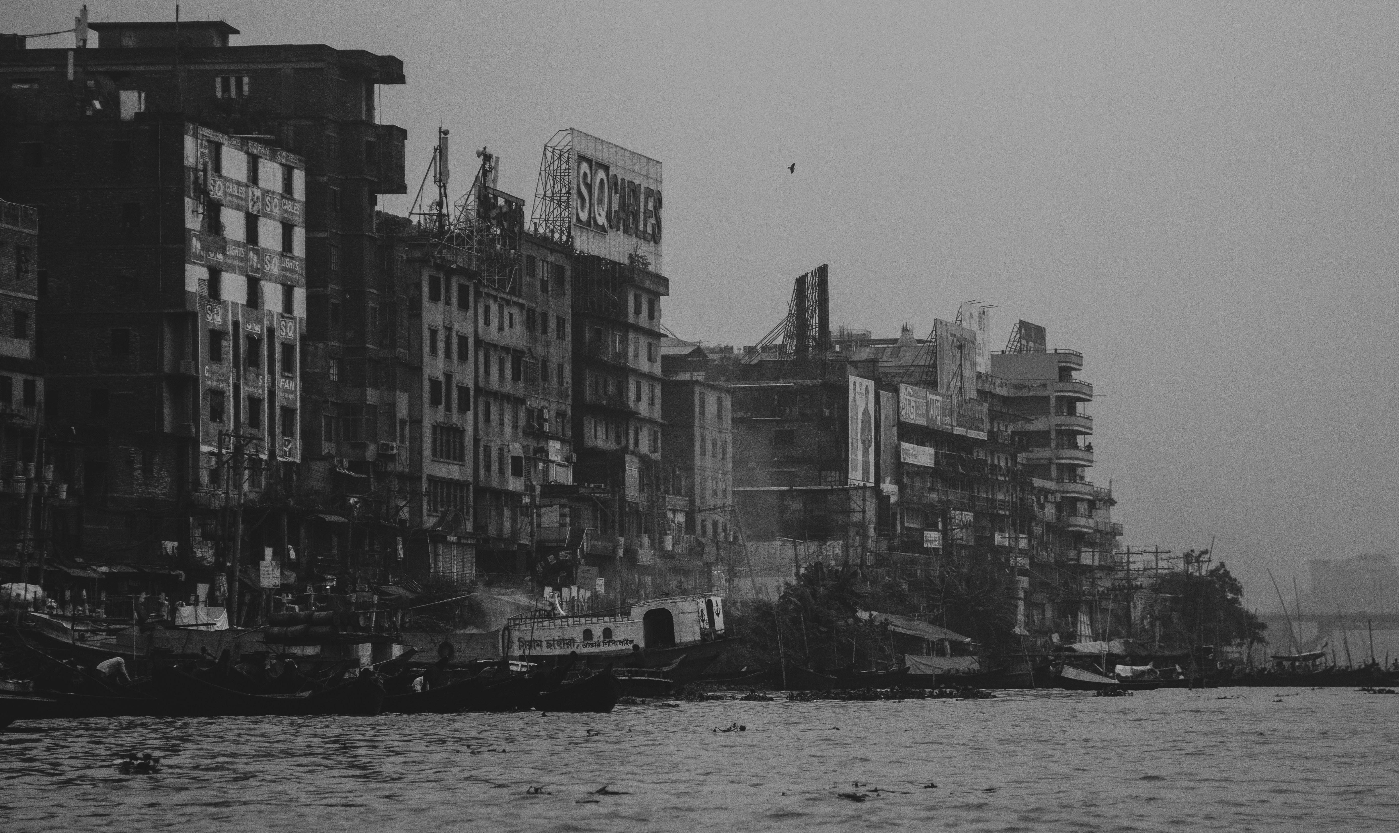 Buildings line a riverbank under a cloudy sky.