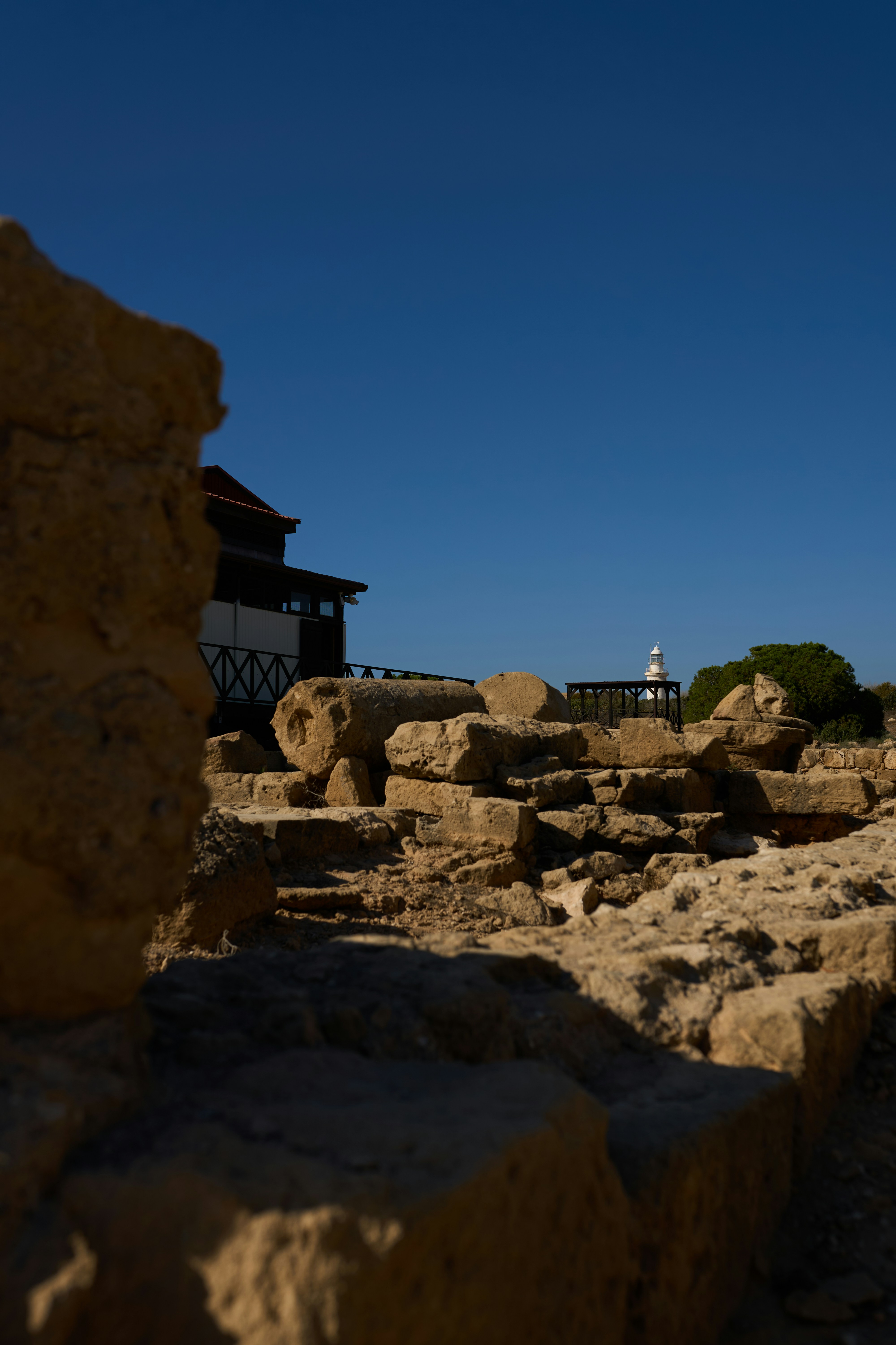 Ancient stone ruins in the foreground with a distant lighthouse and clear blue sky, illustrating a blend of history and maritime heritage.