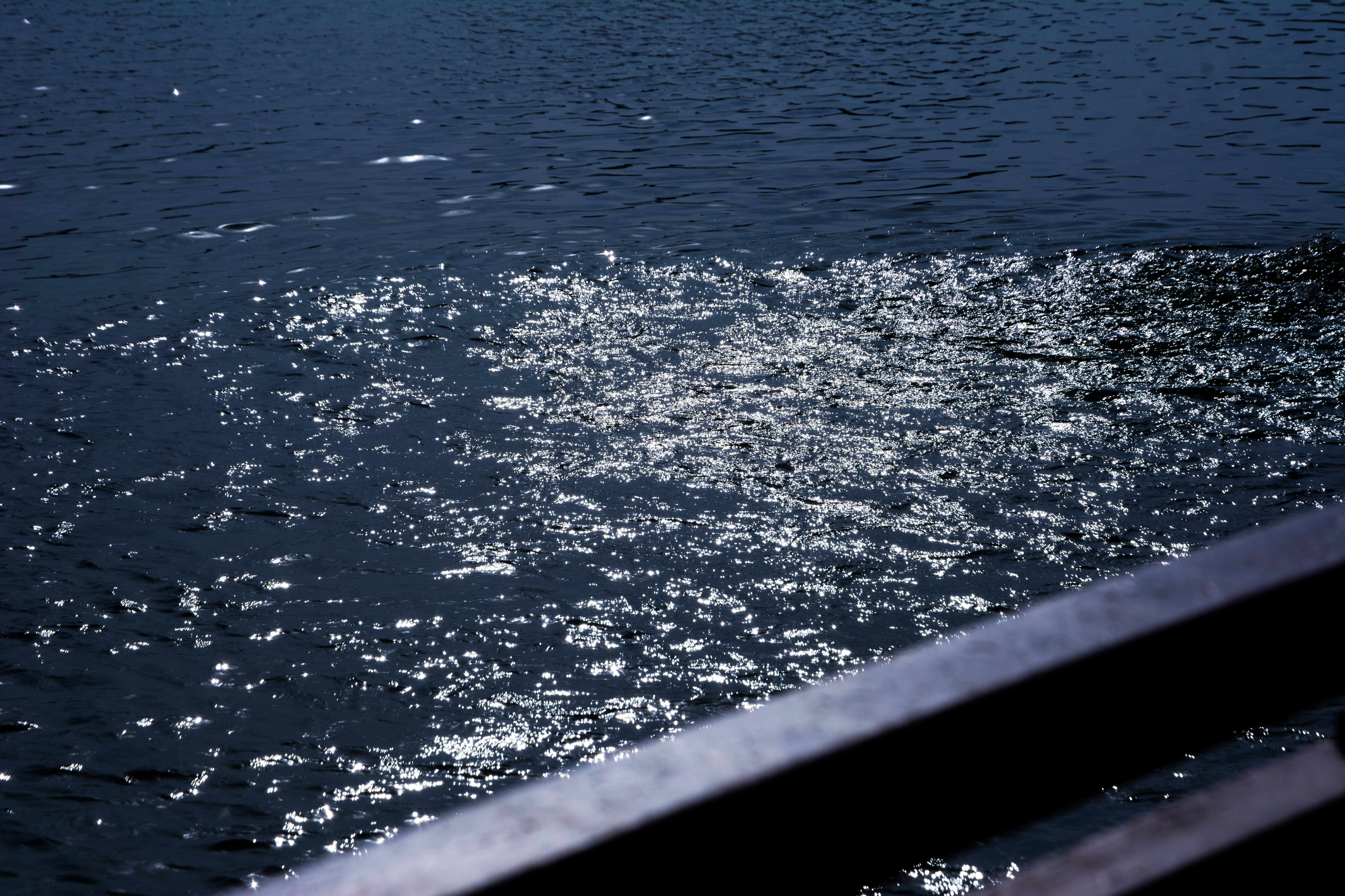 Glistening sunlight dances on the surface of a serene body of water, framed by a wooden railing. The scene captures the essence of tranquility.