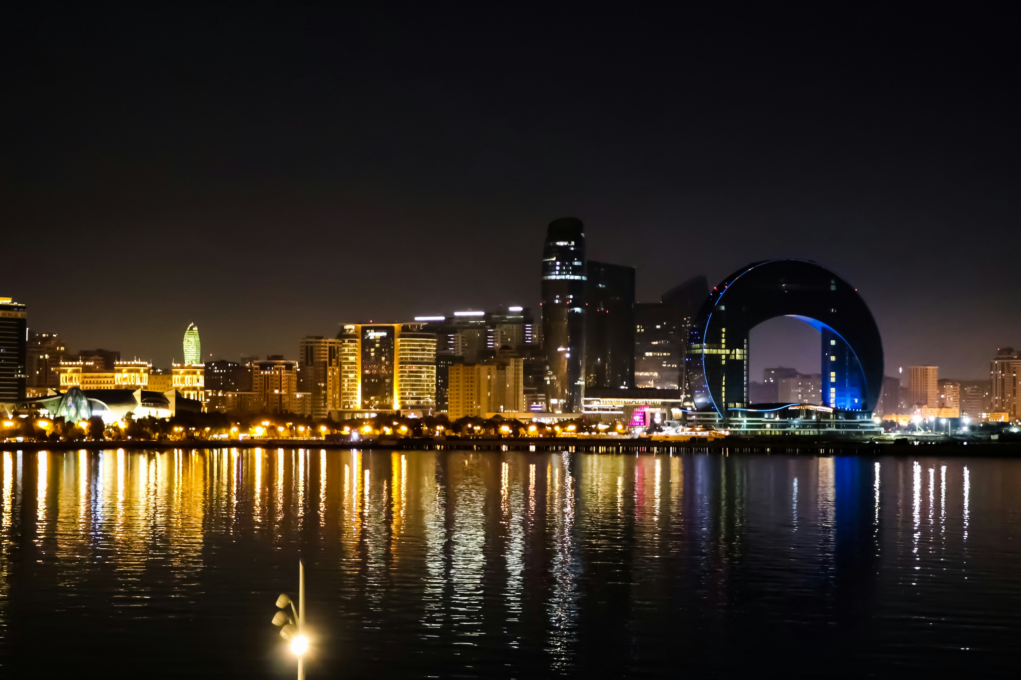 Modern cityscape with illuminated buildings reflected in water at night.