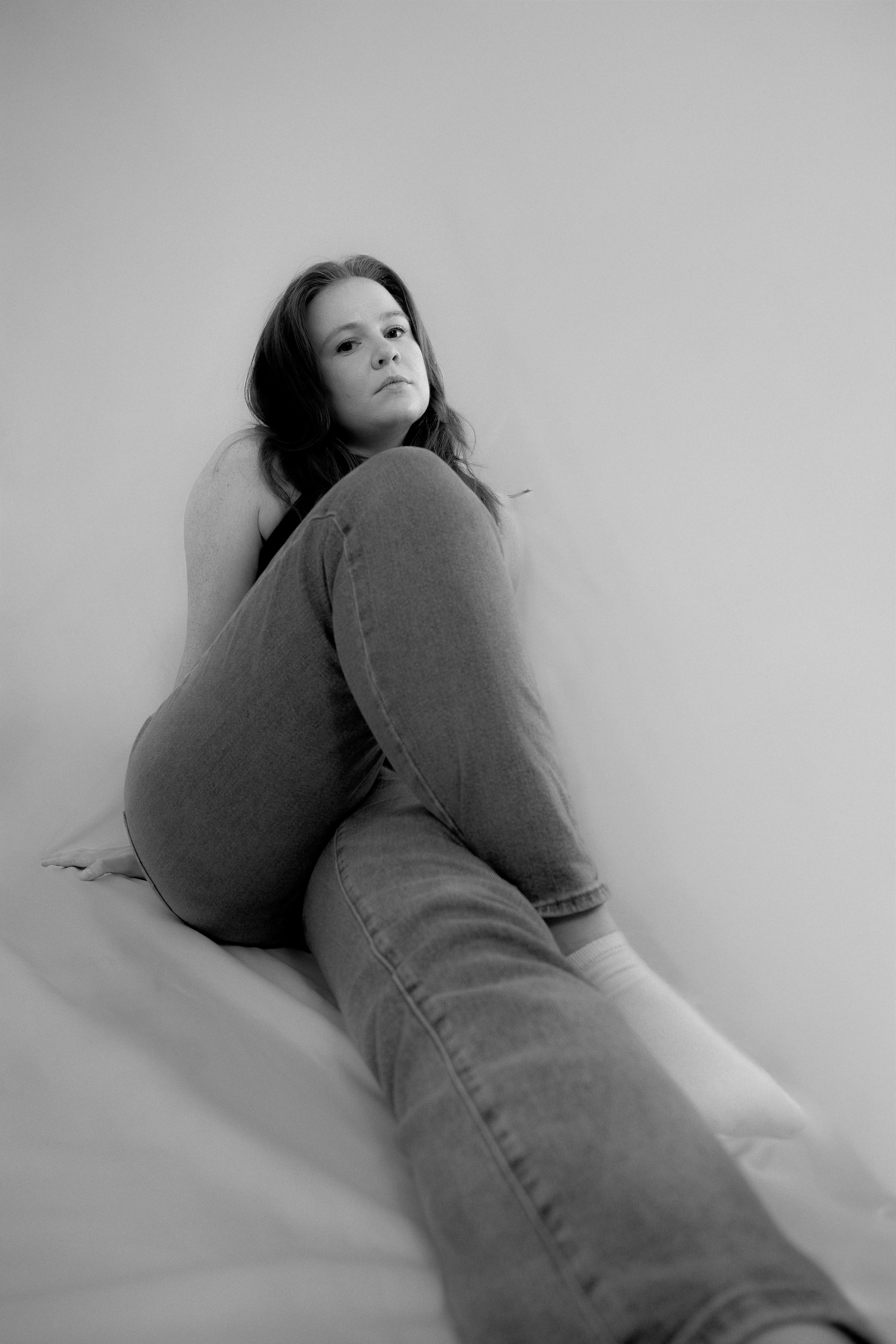 Woman in jeans sits against a plain background