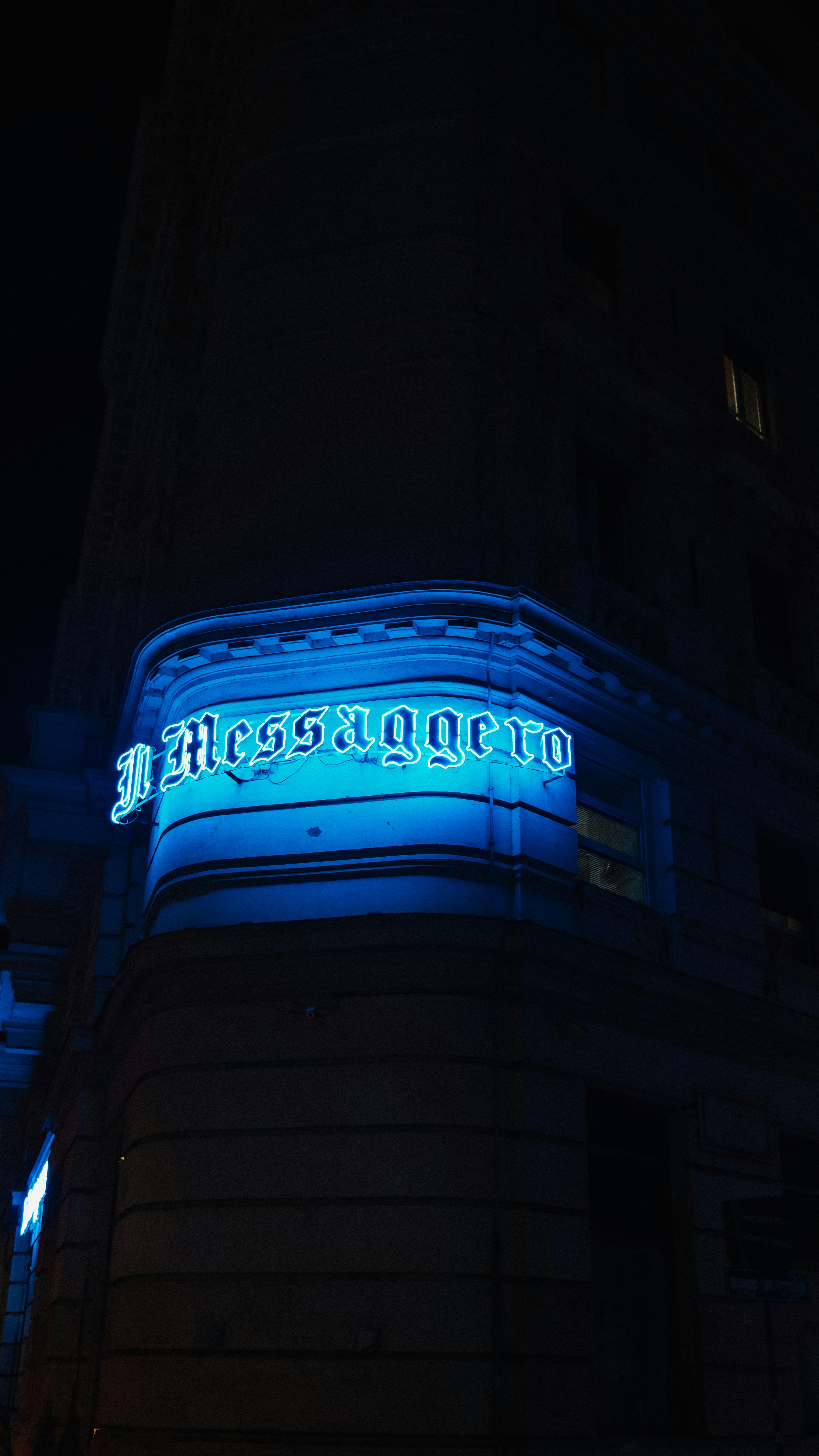 Blue neon sign "il messaggero" on building at night.