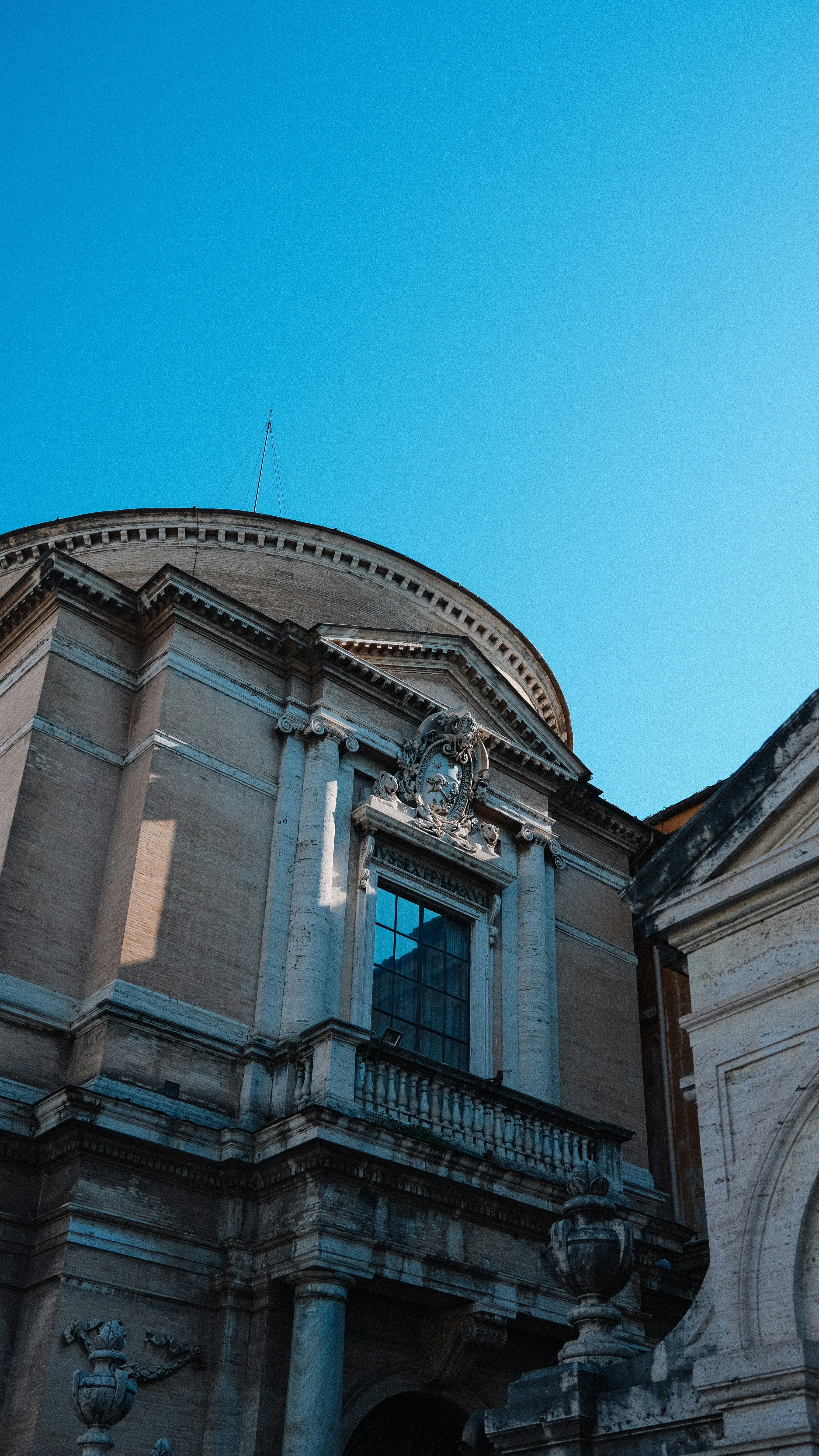 Historic building facade featuring intricate details and a large window, bathed in natural light against a clear blue sky.