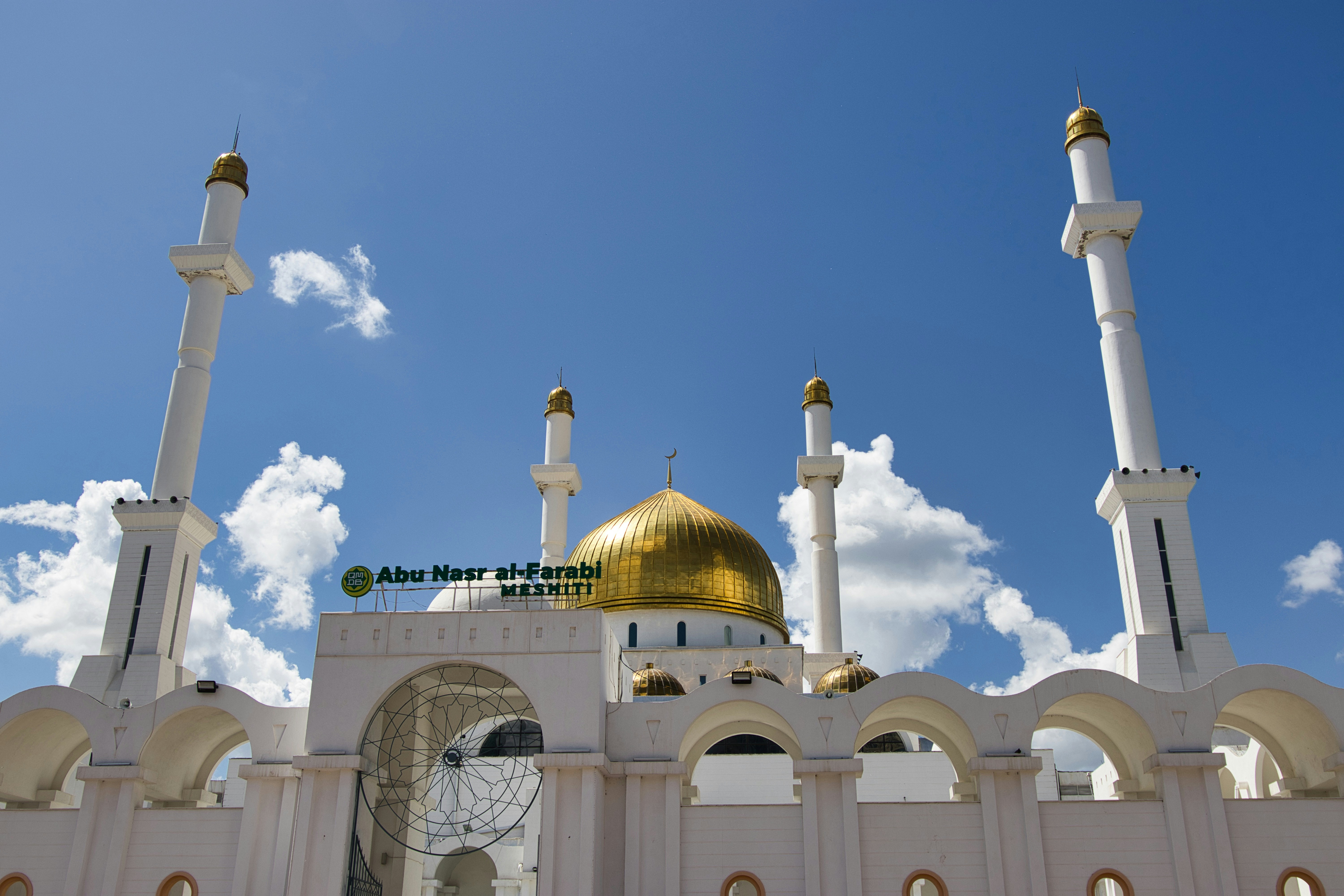 Majestic mosque with a gleaming golden dome and towering minarets, set against a vibrant blue sky with fluffy clouds.