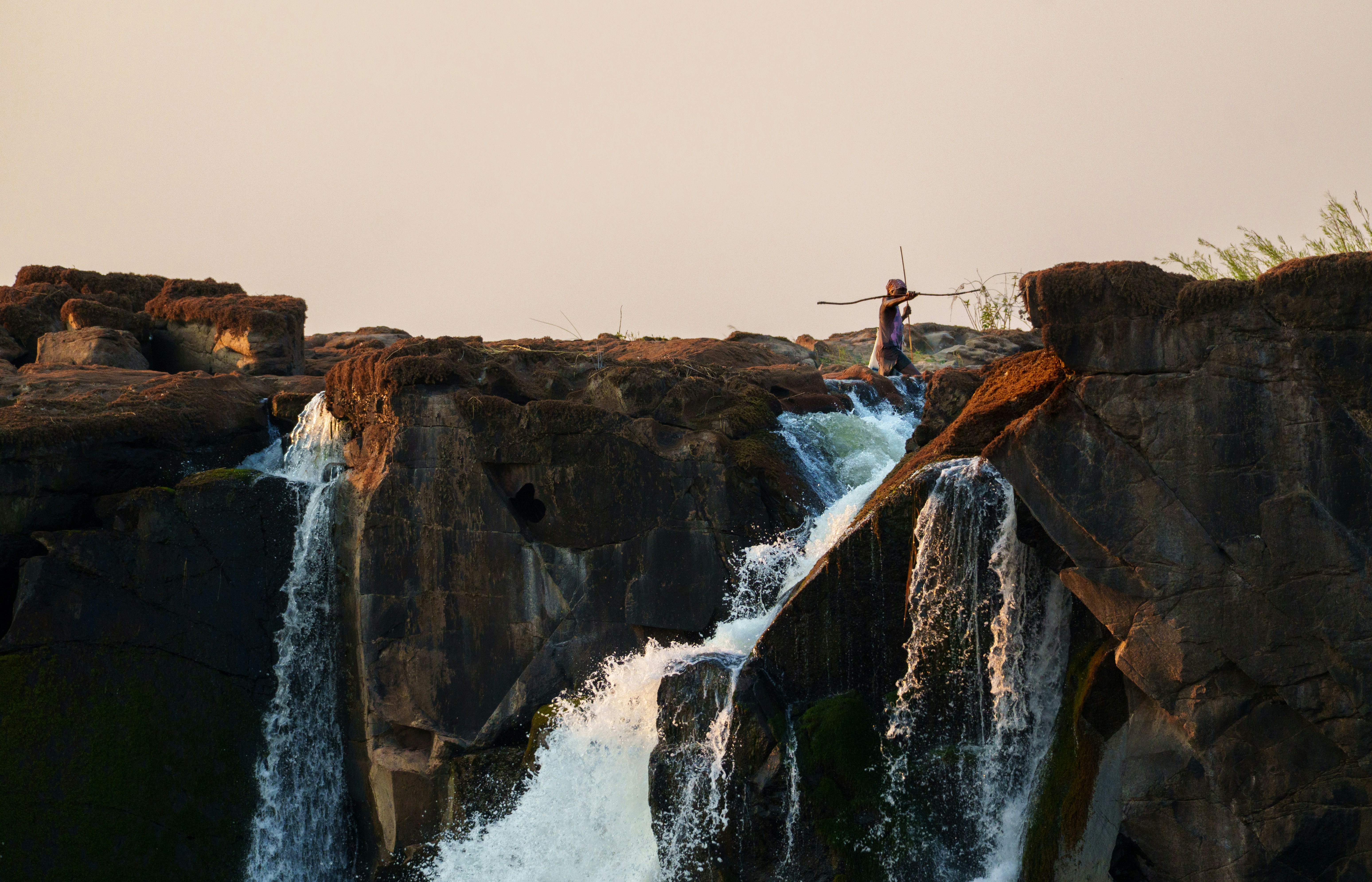 Local tribesman fishing with a net on a stick at the top of Victoria Falls during sunset.