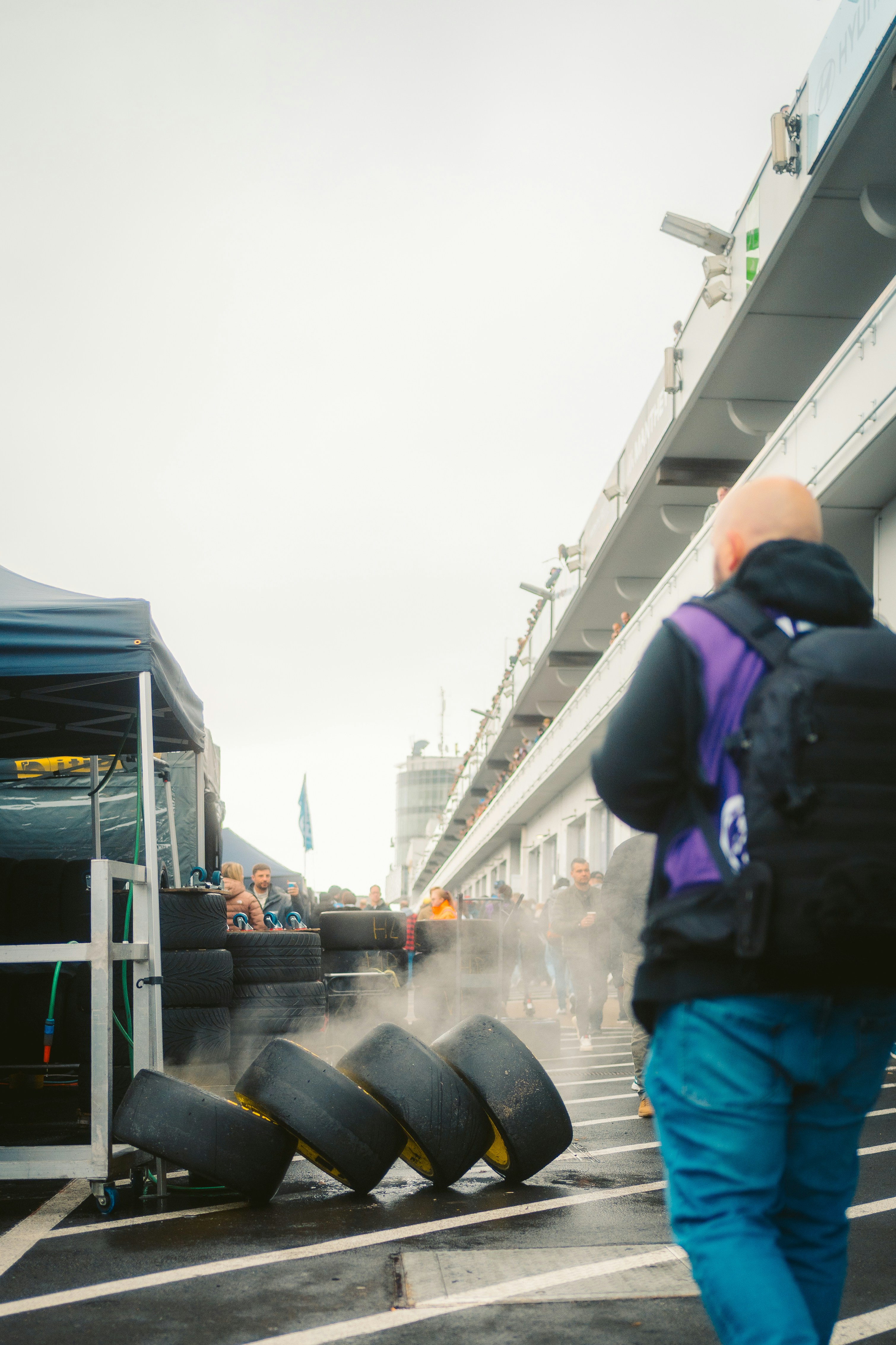 Pit-Lane Reverie: Stacked Tires, Steam, and a Quiet Figure