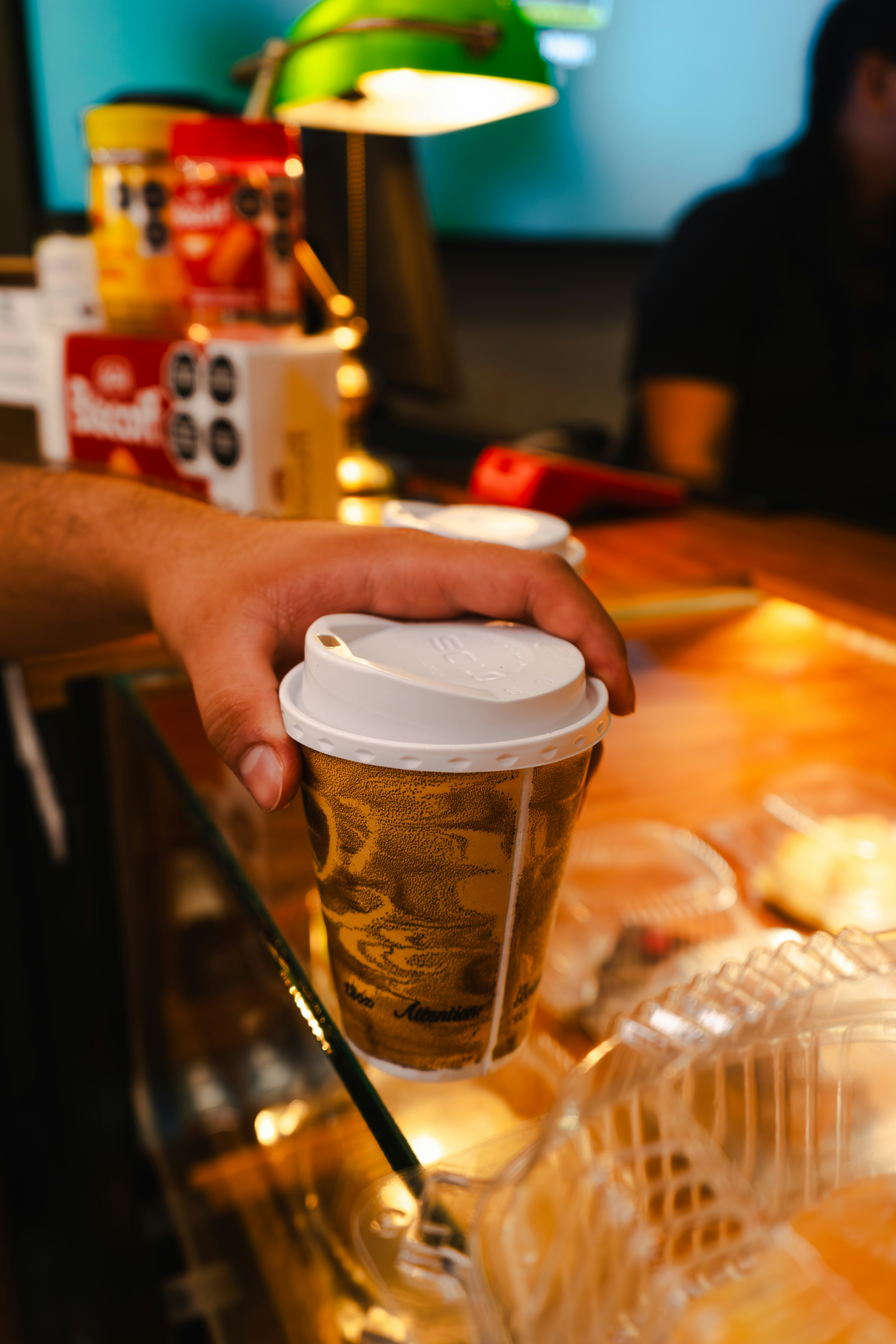 Hand holding a takeaway coffee cup over counter.