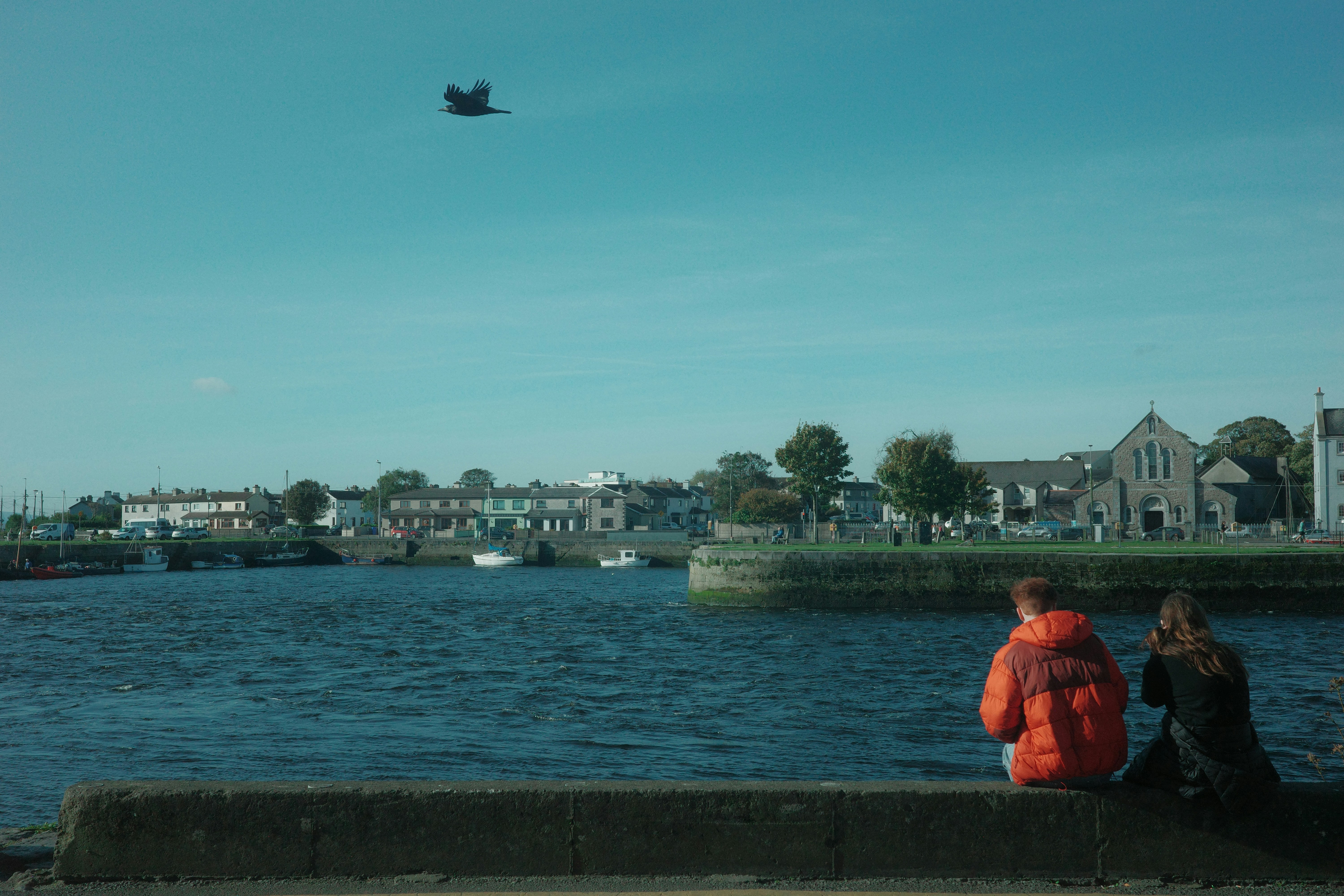 Red Jacket at the Seawall: Harbor Quiet Under a Distant Helicopter