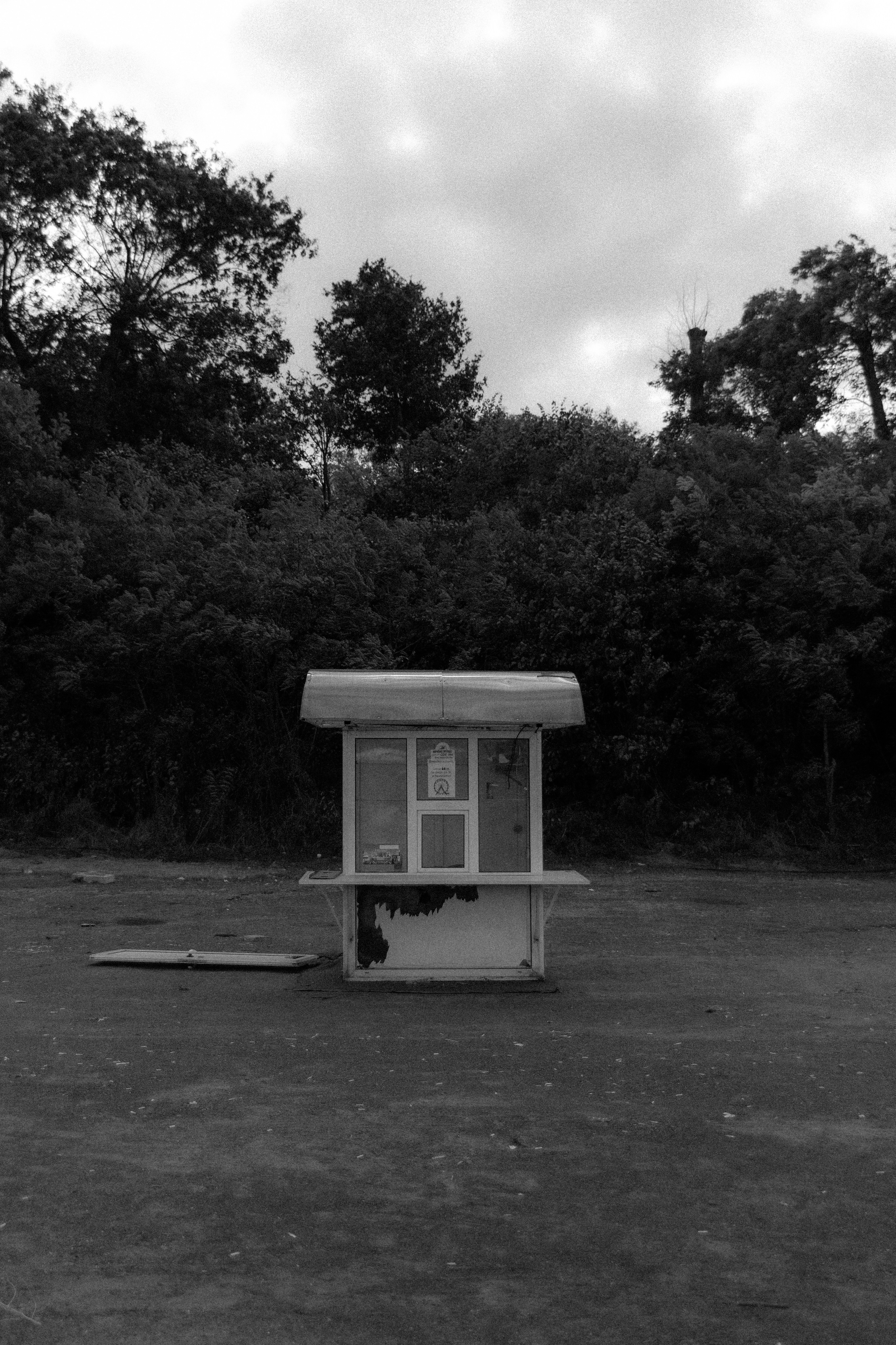 Abandoned kiosk stands in a desolate landscape.