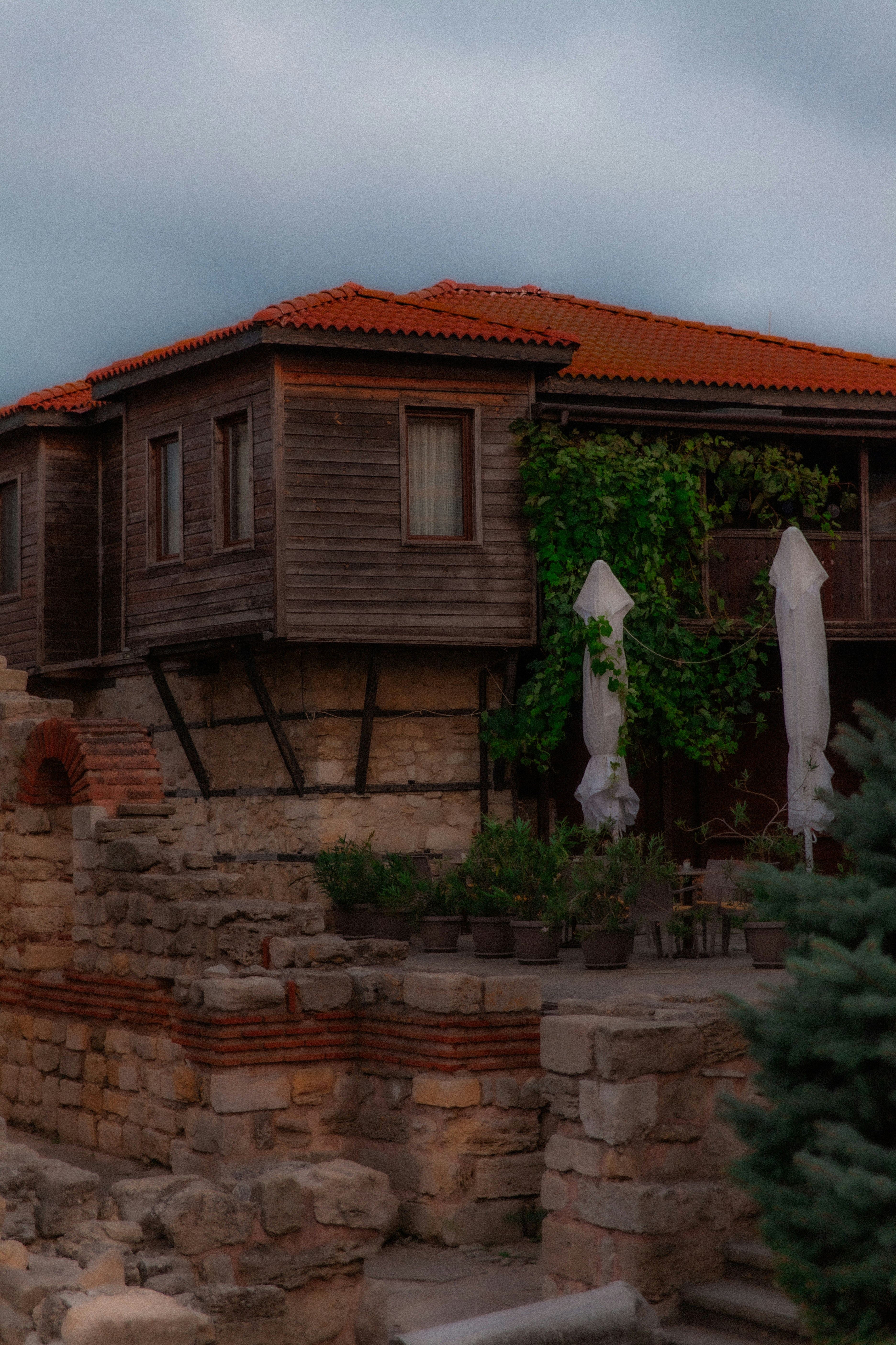 Old wooden house with stone ruins and umbrellas.
