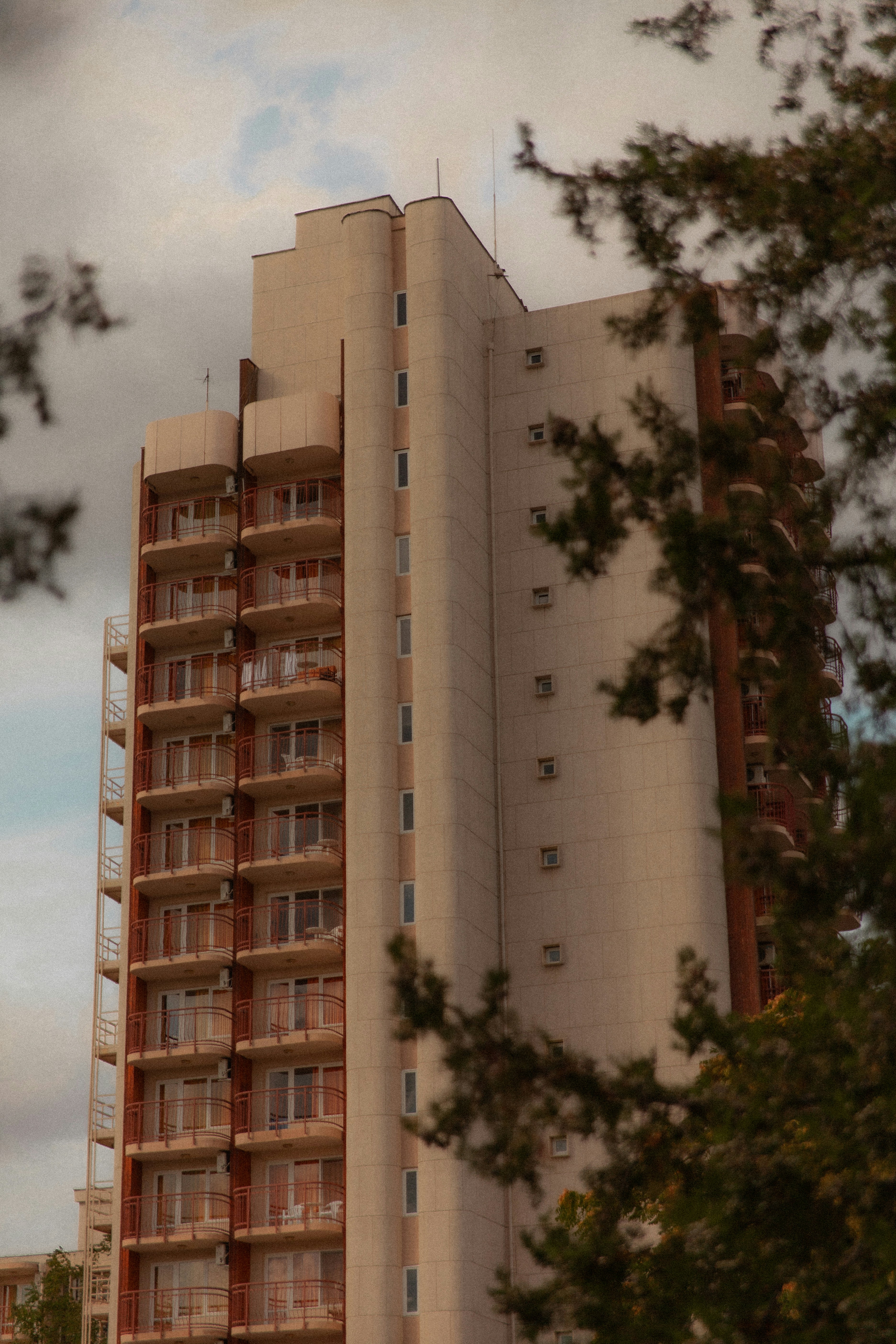 Tall apartment building with balconies framed by trees