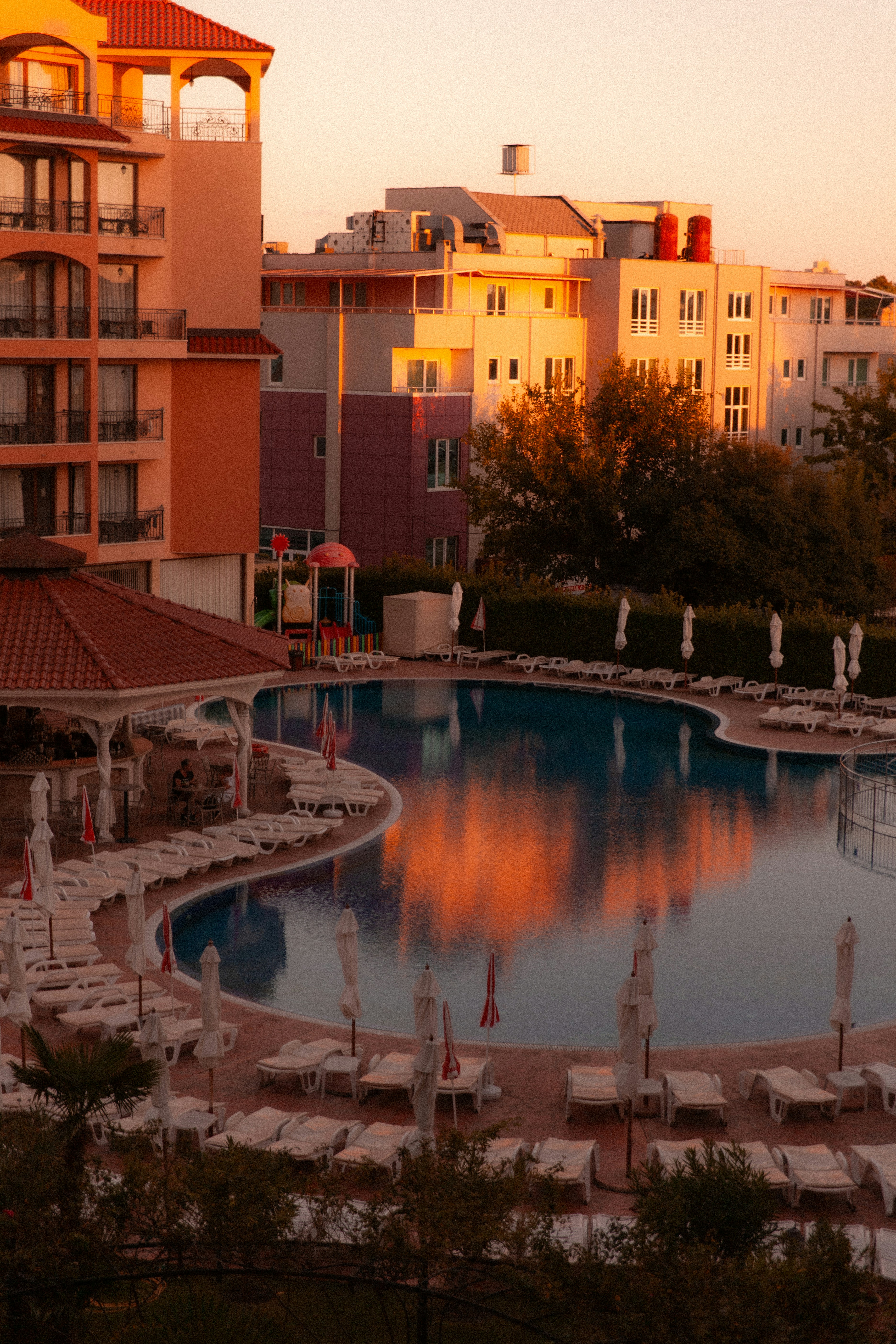 Resort swimming pool with buildings at sunset.