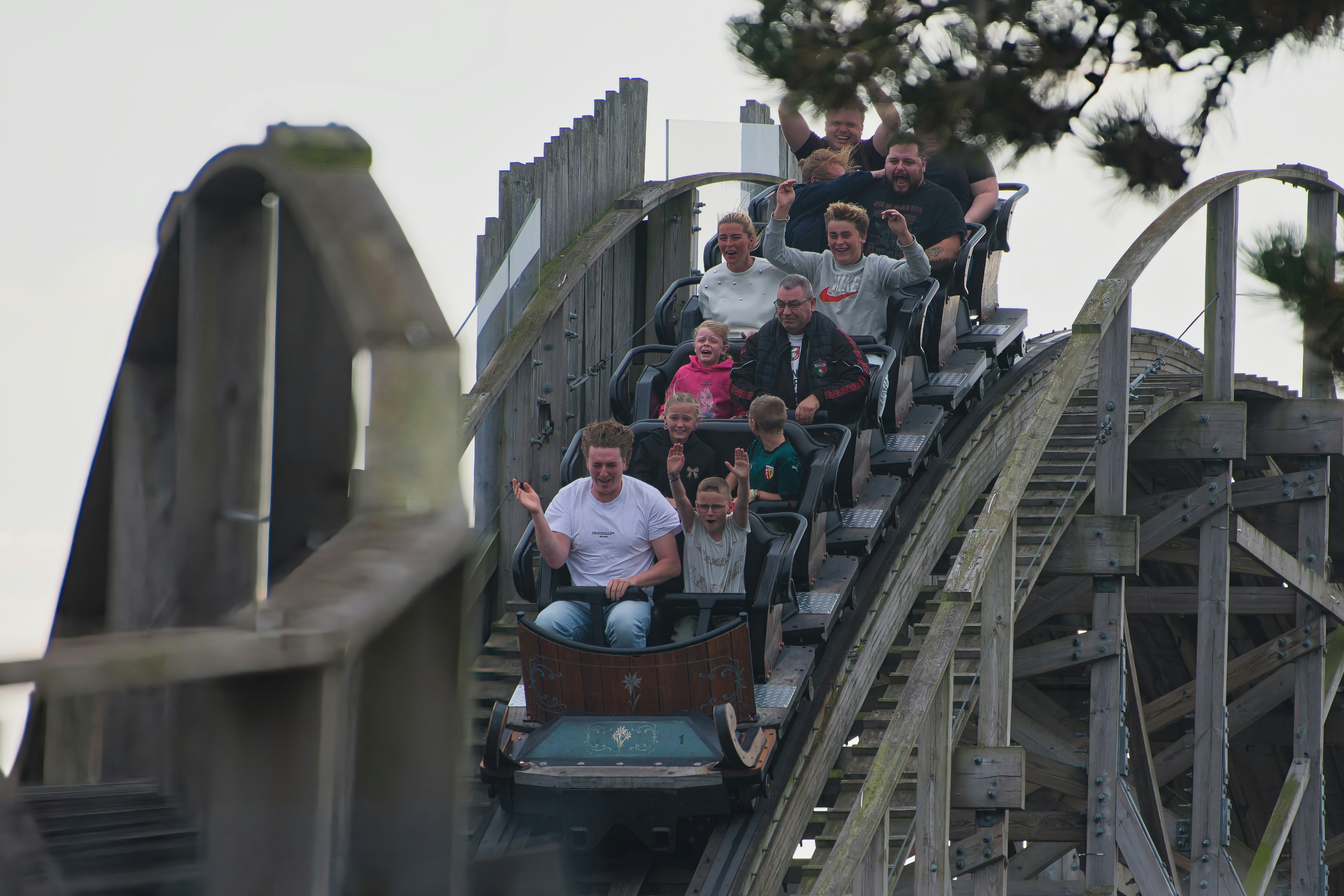 Thrill-seekers experiencing the exhilarating drop on a wooden roller coaster, capturing moments of joy and excitement.