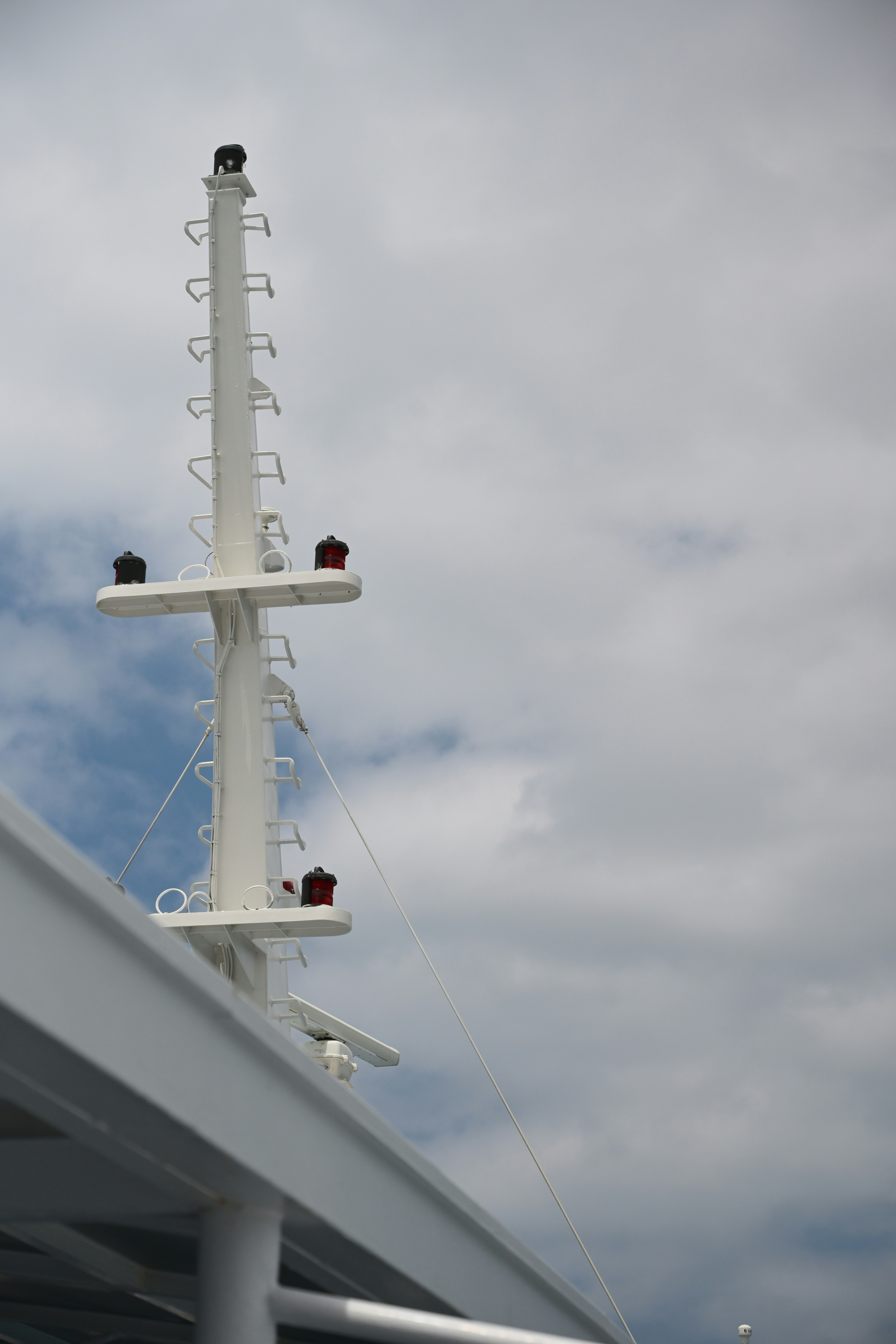 White ship mast with red lights against cloudy sky
