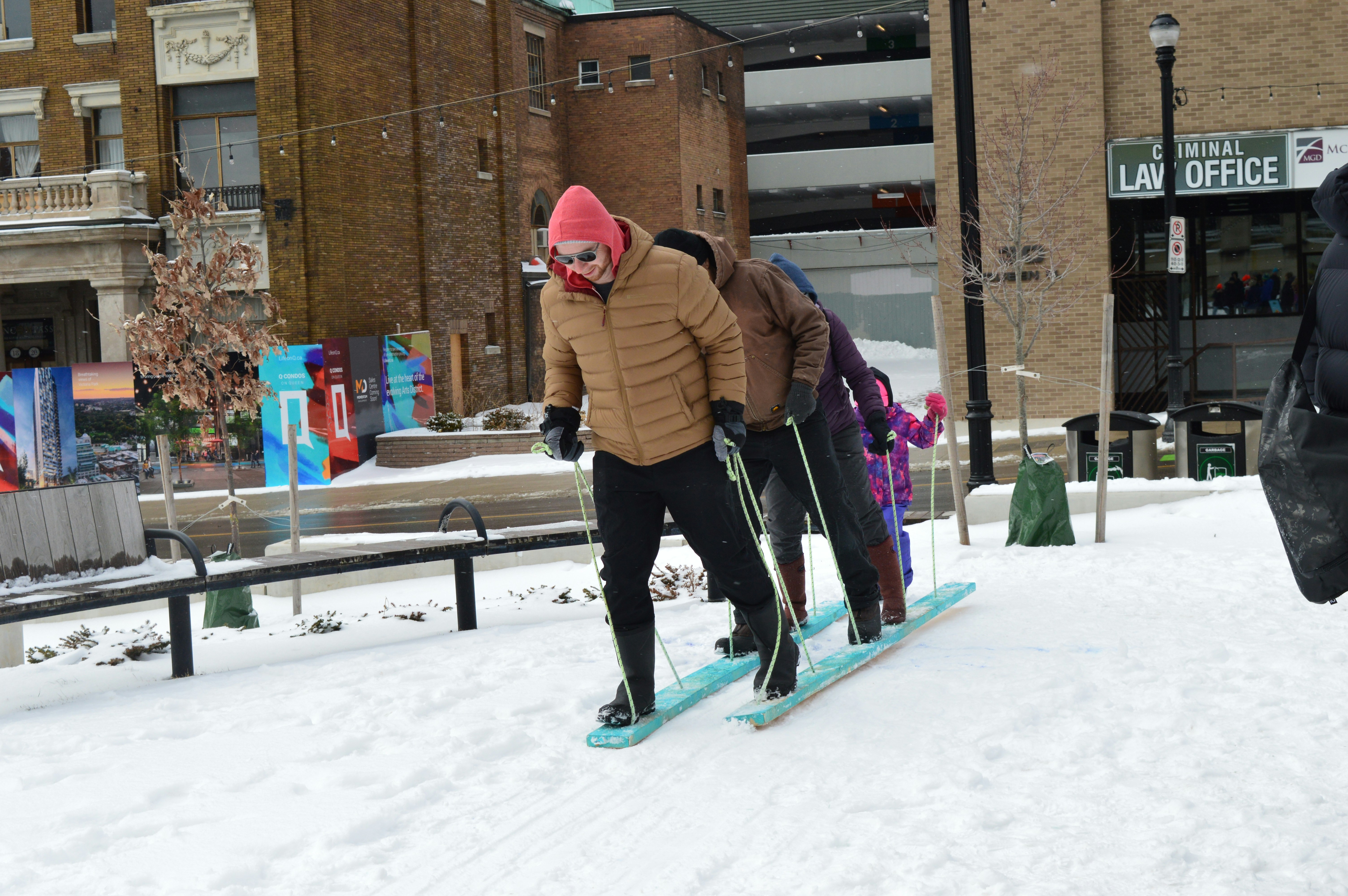 Three individuals navigating a snow-covered urban landscape on sleds, showcasing a playful winter activity.