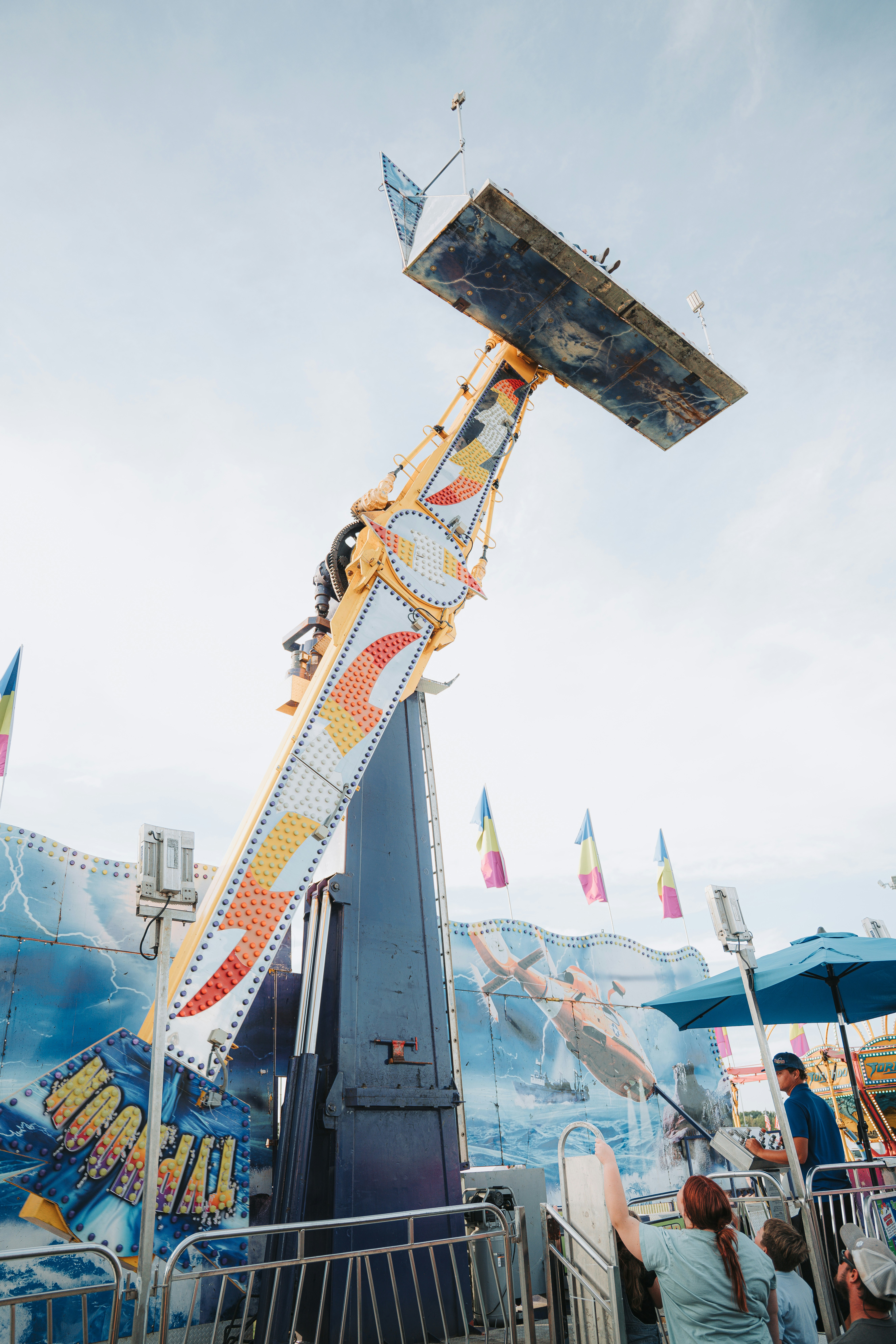 A carnival ride towers against a clear sky, with riders preparing for an exhilarating experience. Colorful decorations and playful elements enhance the festive atmosphere.