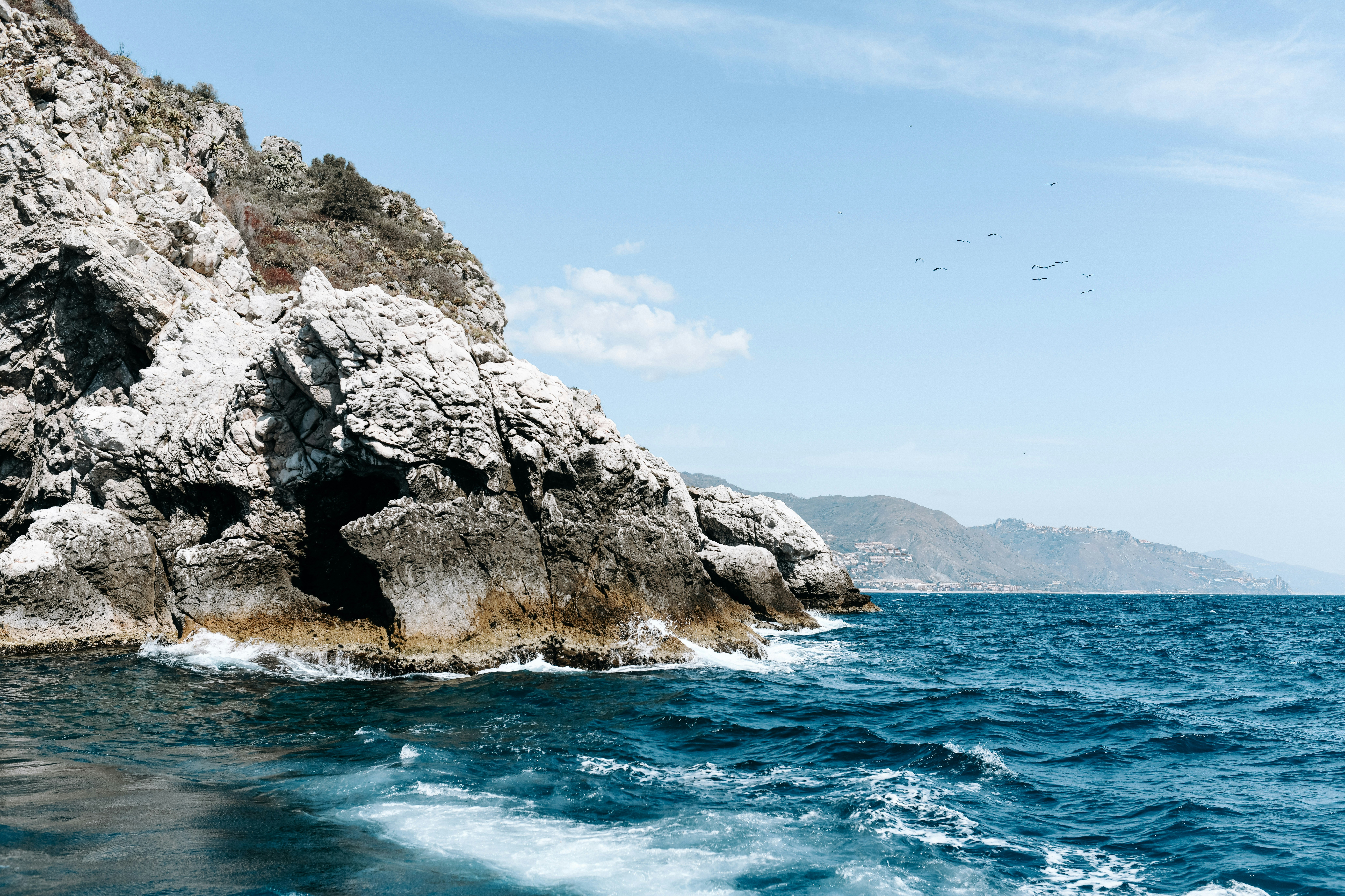 Rugged coastline meets vibrant blue waters under a clear sky, showcasing the interplay of natural textures and colors.