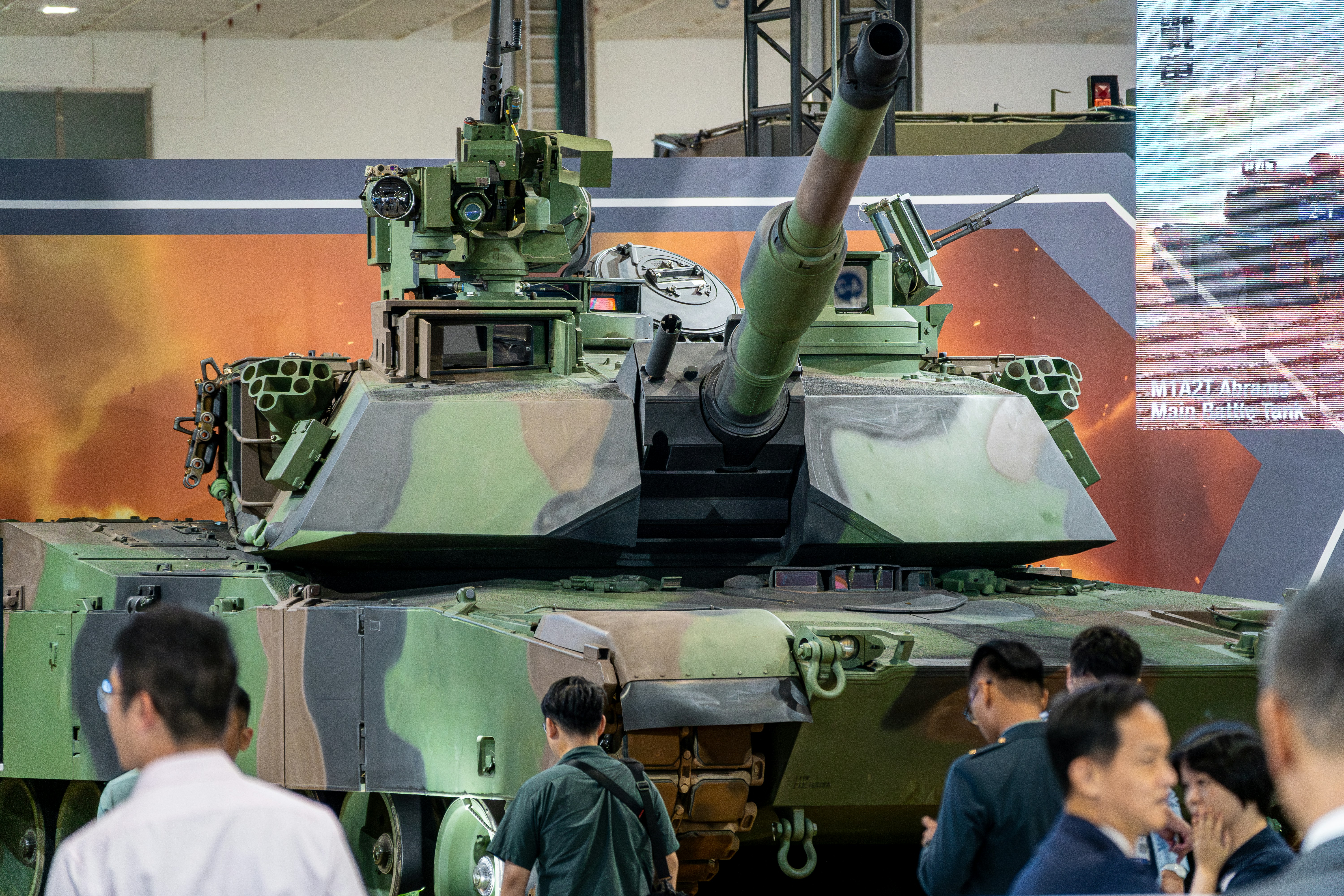 Camouflaged military tank on display with people around.