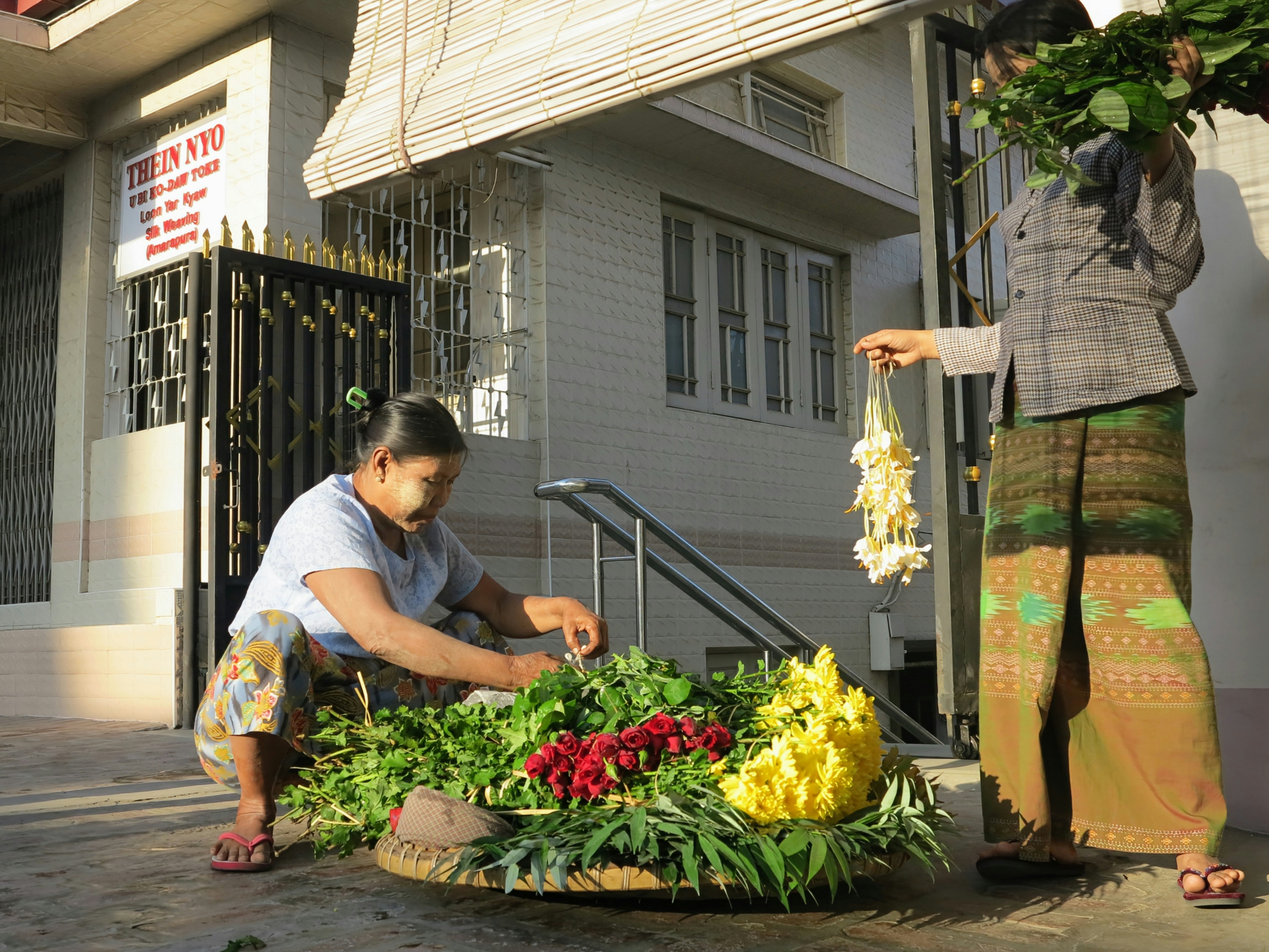 Two women arrange flowers and plants at a market.