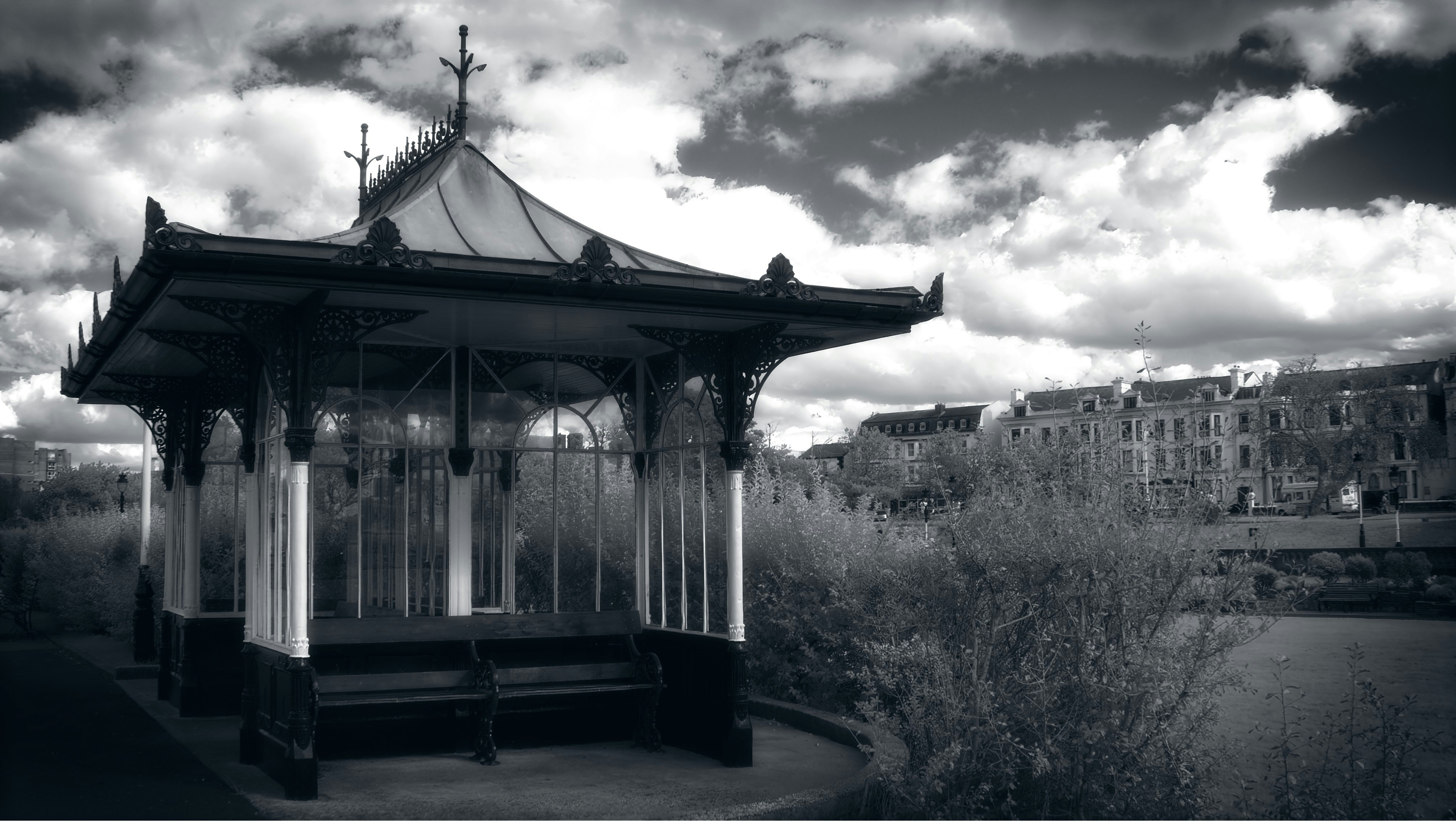 Victorian-style gazebo surrounded by lush greenery and dramatic clouds, evoking a sense of nostalgia and tranquility.