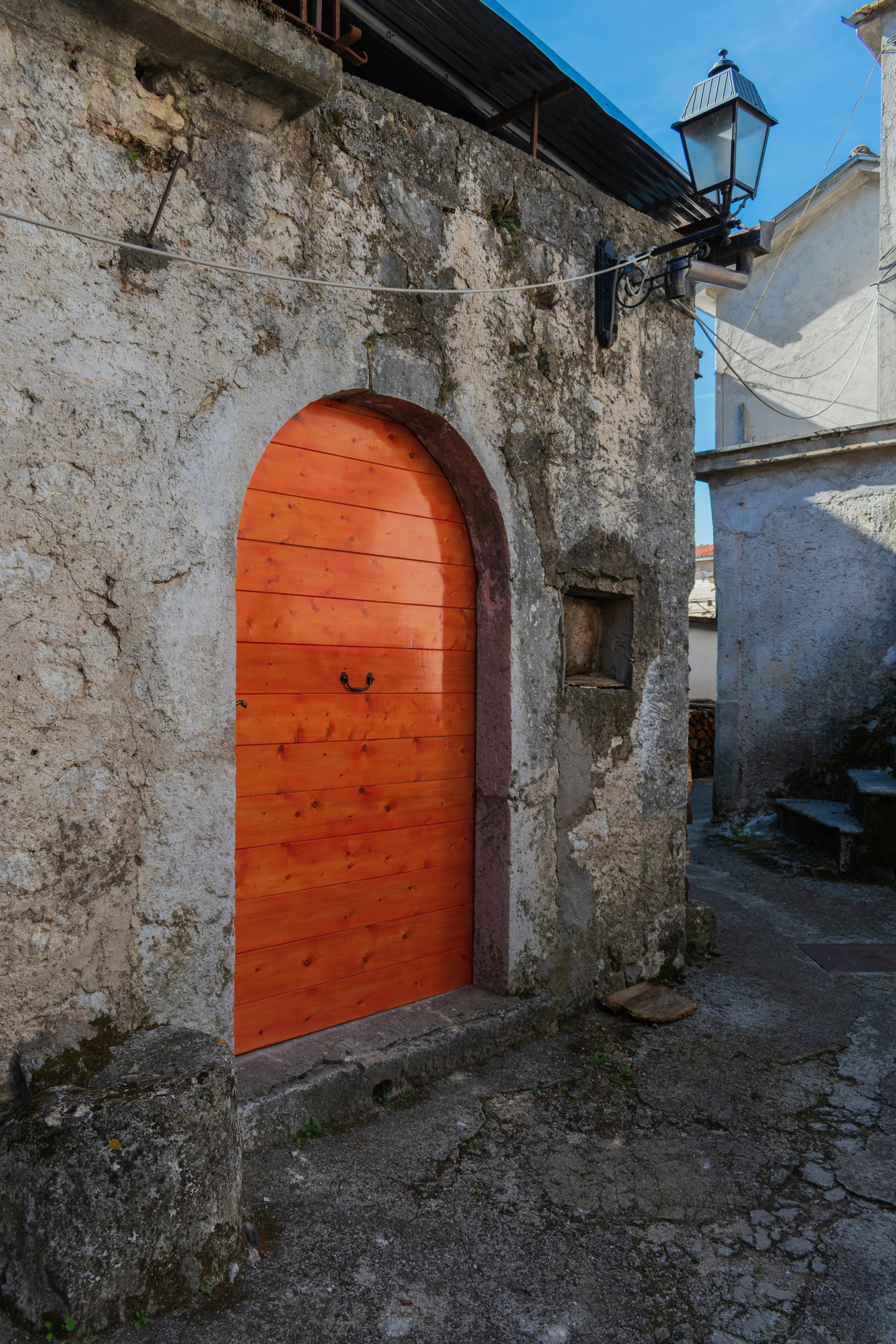 An arched orange wooden door on a stone building.