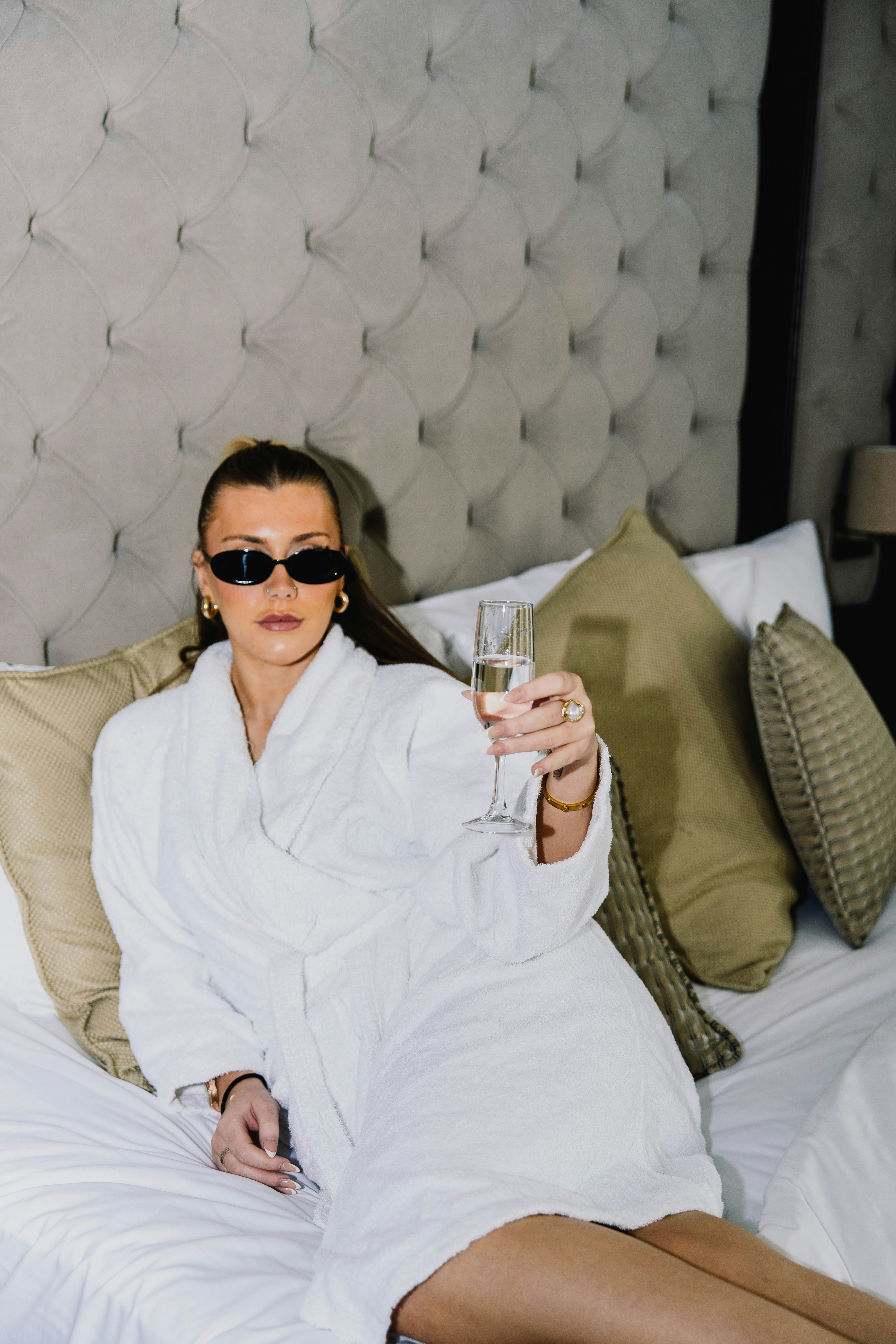 Woman in bathrobe holding champagne glass on bed.