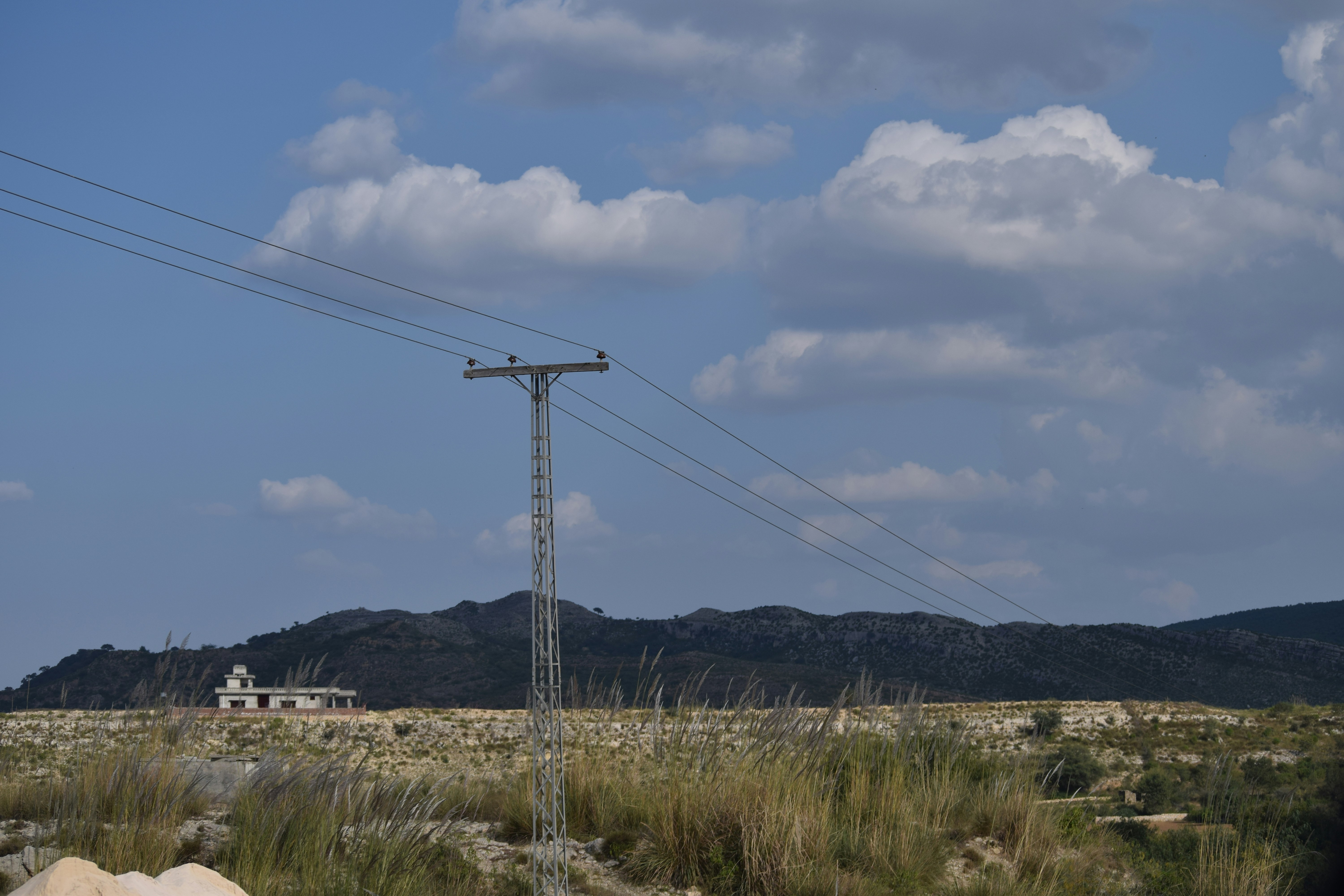 Power lines cross a dry, hilly landscape under clouds.