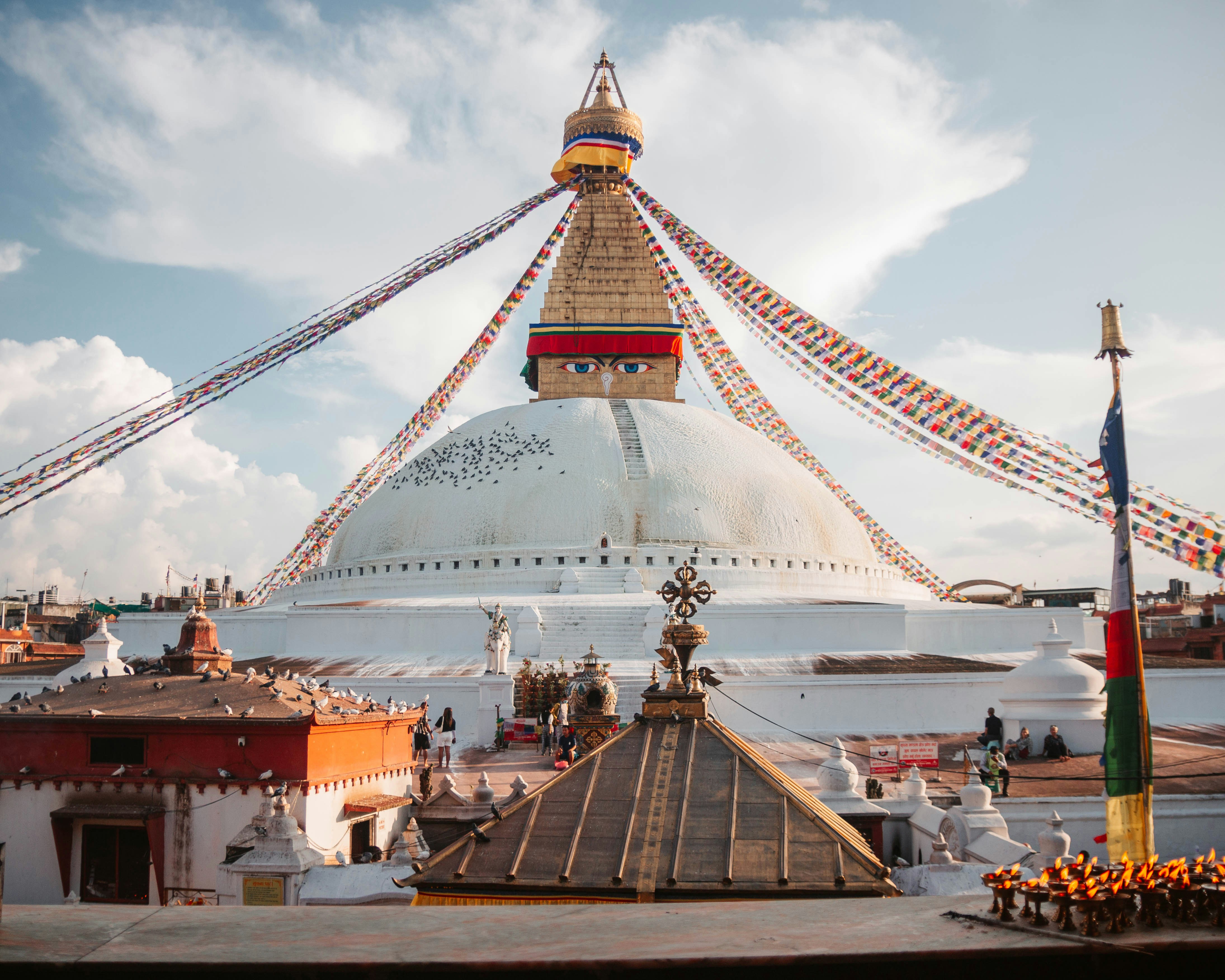 A serene capture of the Boudhanath Stupa in Kathmandu, Nepal, one of the largest spherical stupas in the world. Prayer flags flutter in the wind above the iconic dome, while the watchful Buddha eyes overlook the city, symbolizing peace, spirituality, and timeless culture. | Large stupa with prayer flags under a blue sky