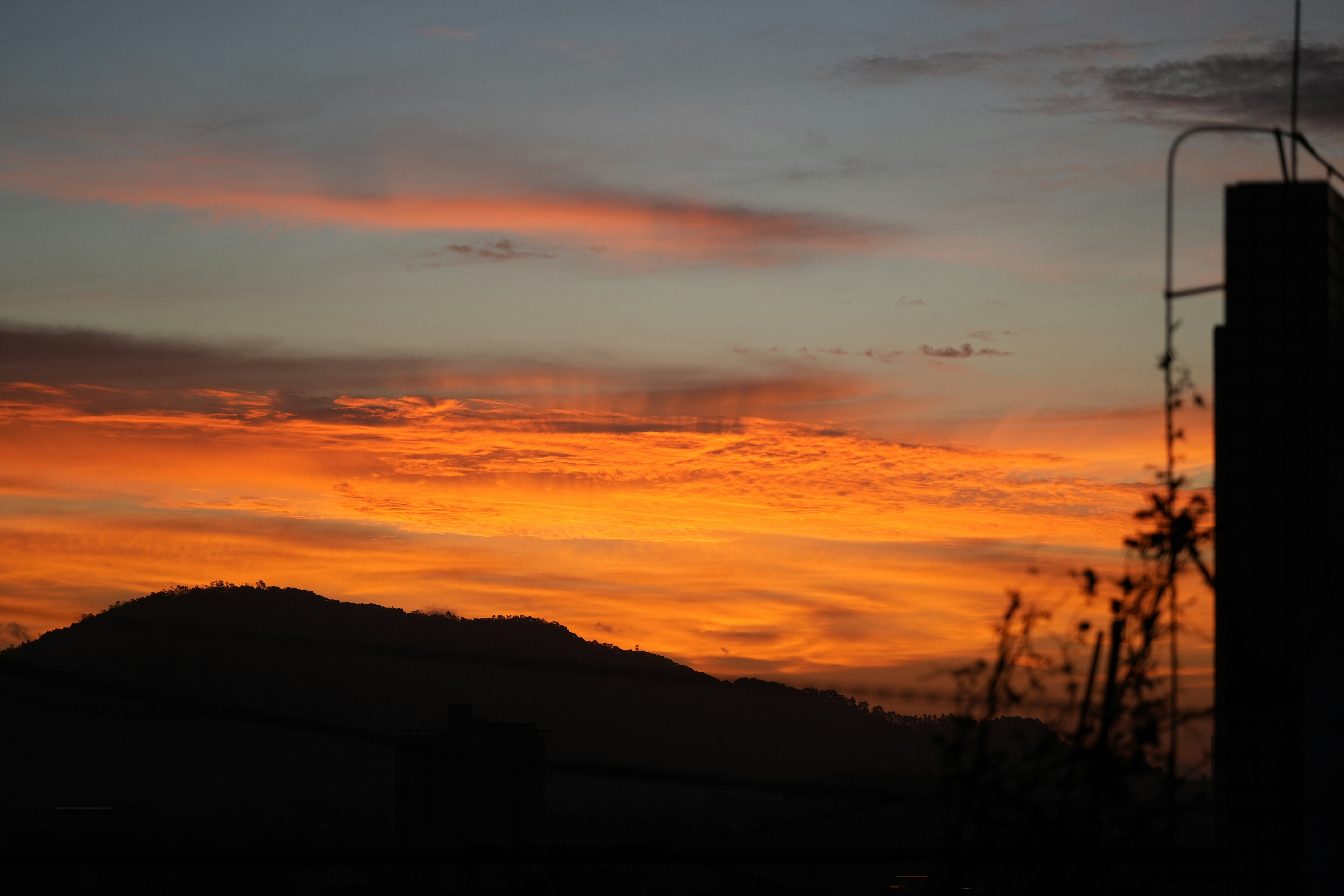 Beautiful sunrise glow... | Vibrant sunset sky over silhouetted mountain and building.