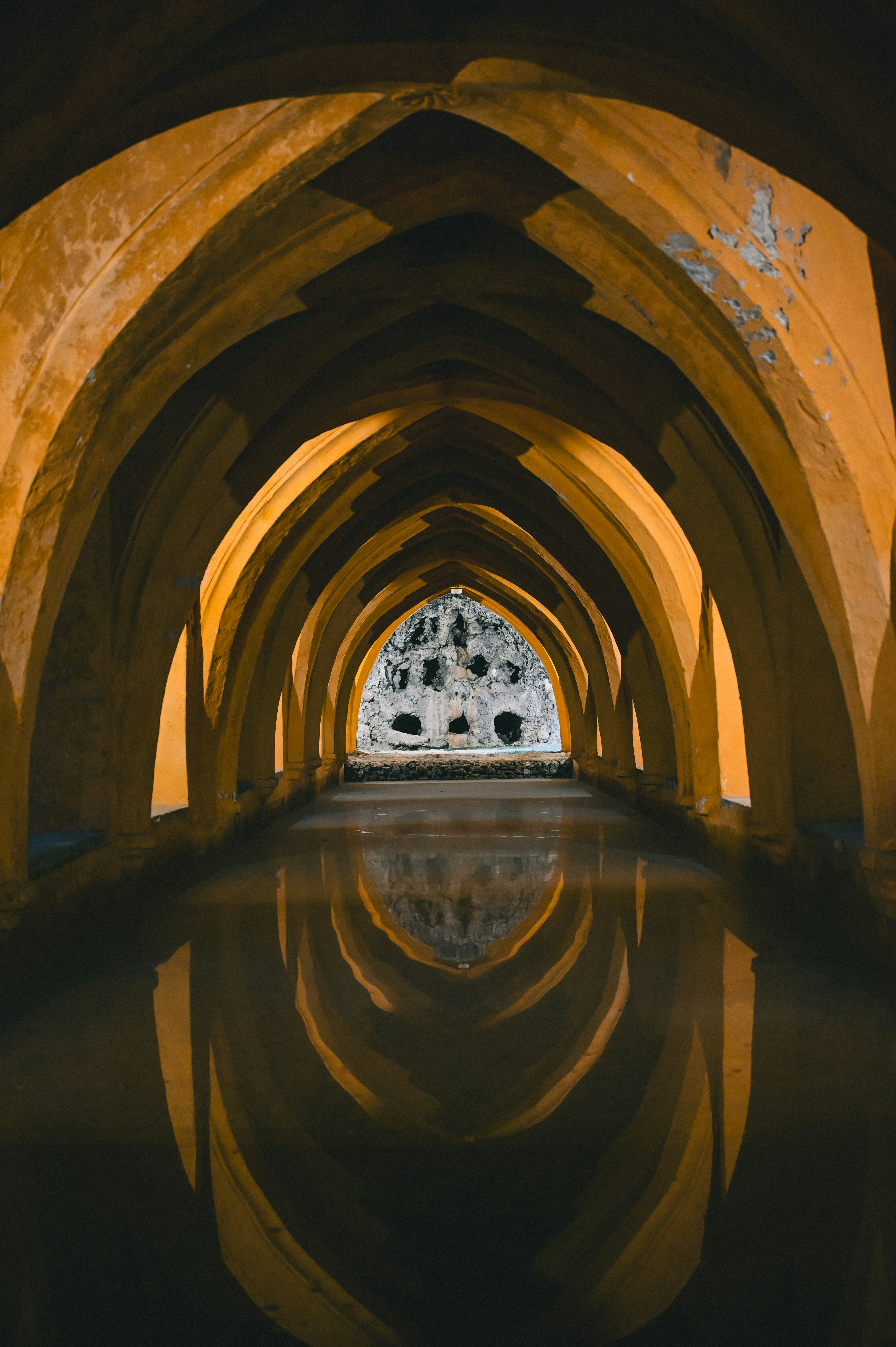 Arched hallway with water reflection and distant opening.