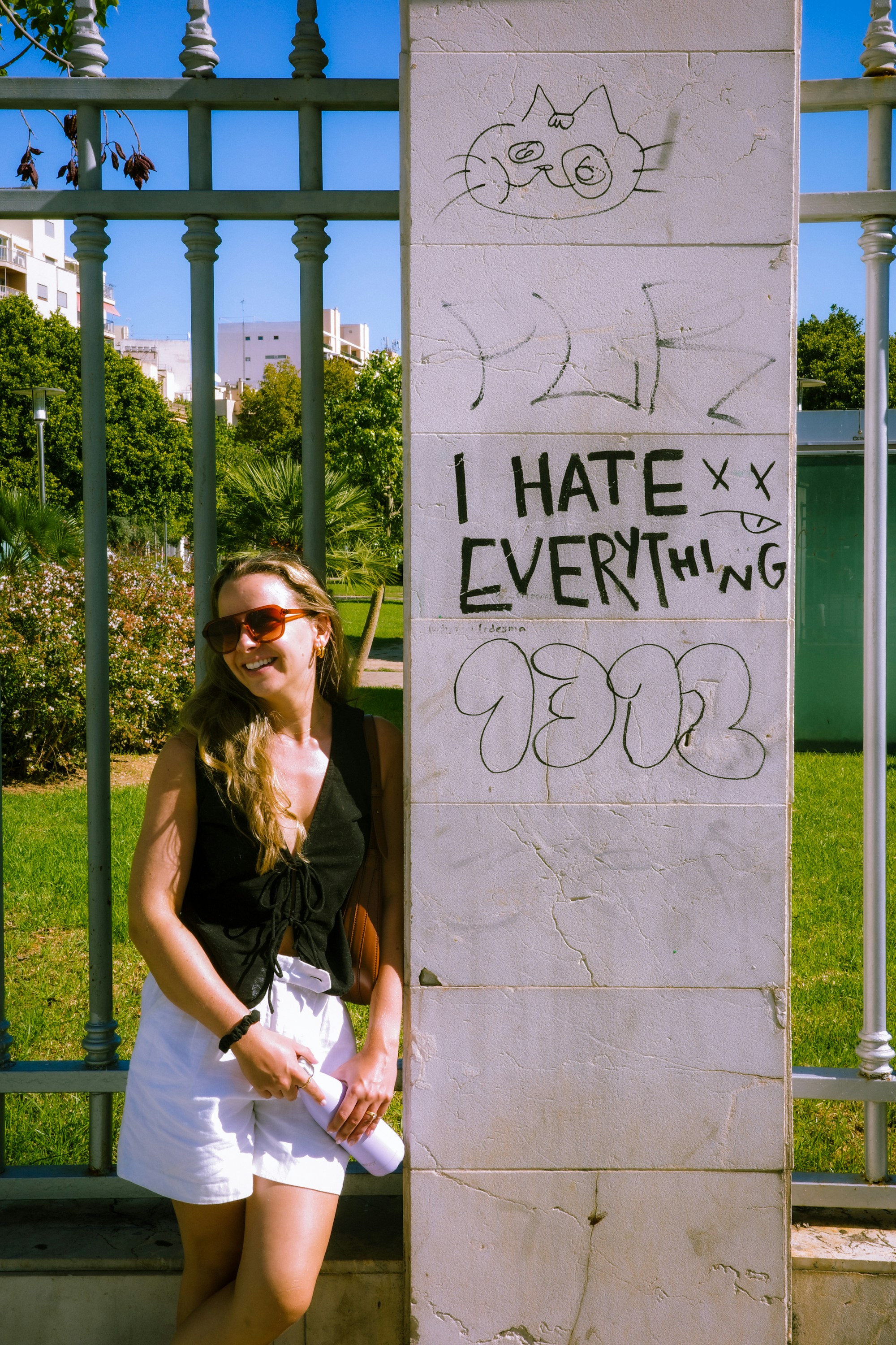 Woman leans against wall with graffiti in park.