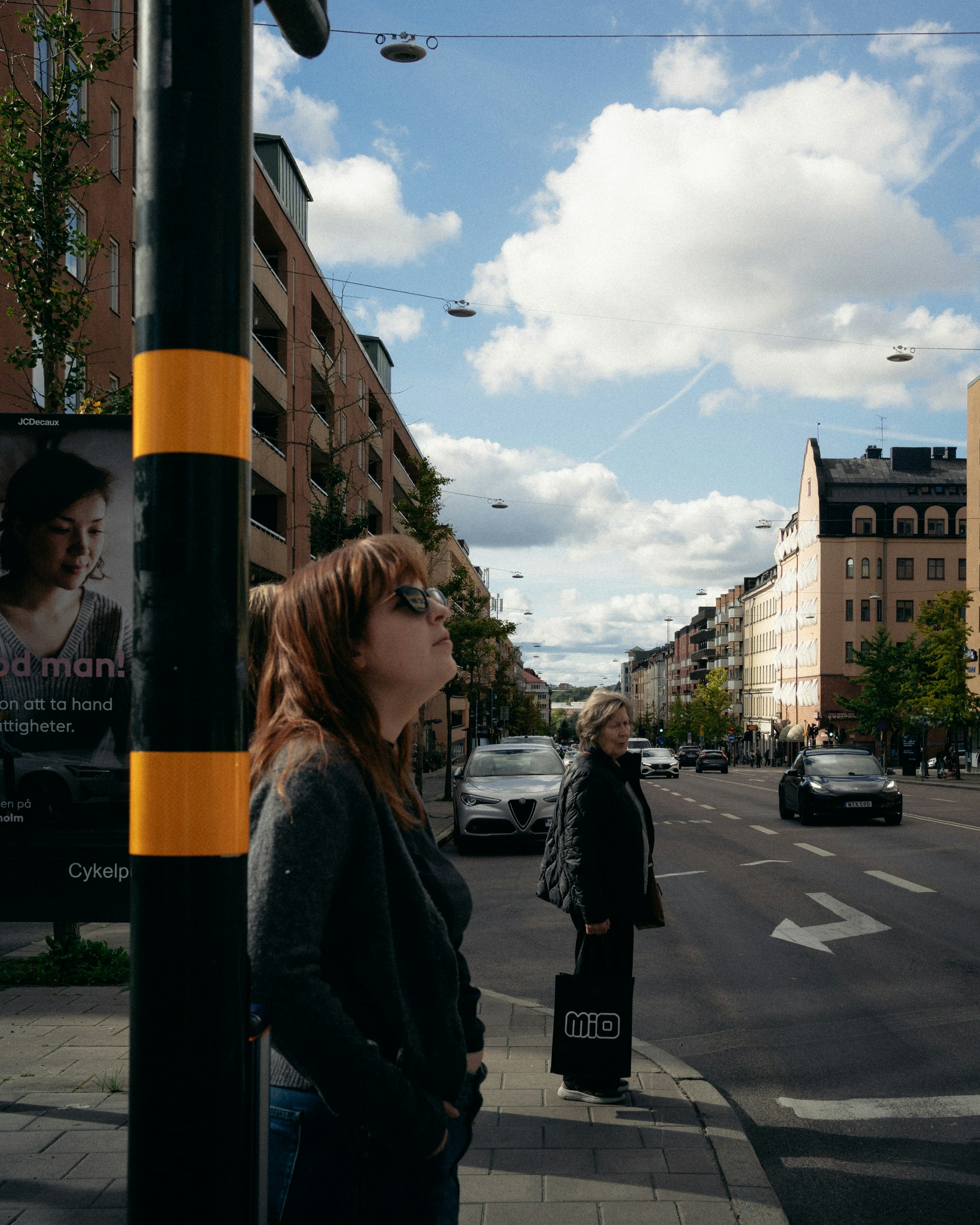 People wait at a sunny city street corner.