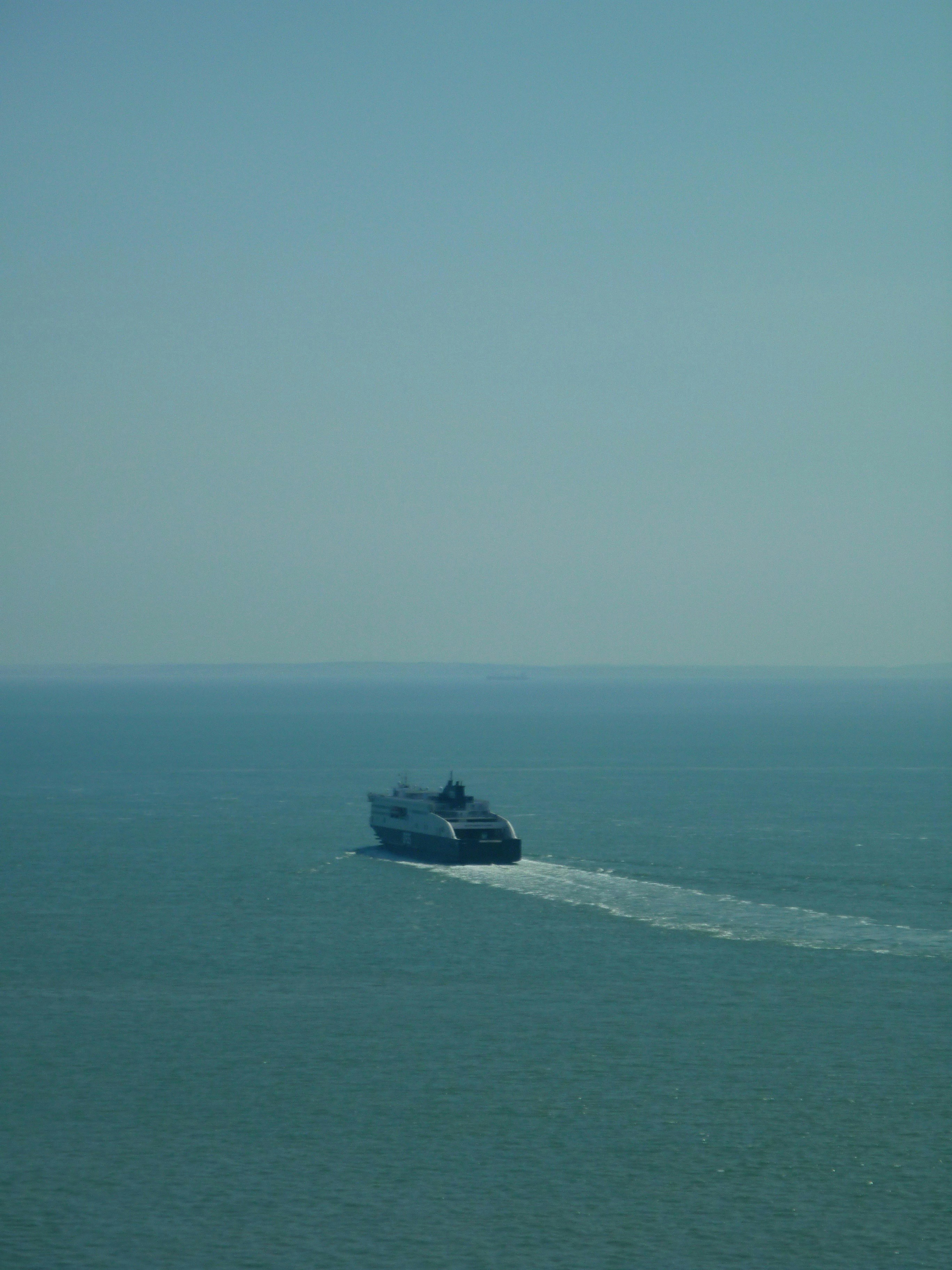 A sleek ferry glides through calm sea waters, leaving a gentle wake behind. The horizon blends seamlessly with the sky, creating a serene backdrop.