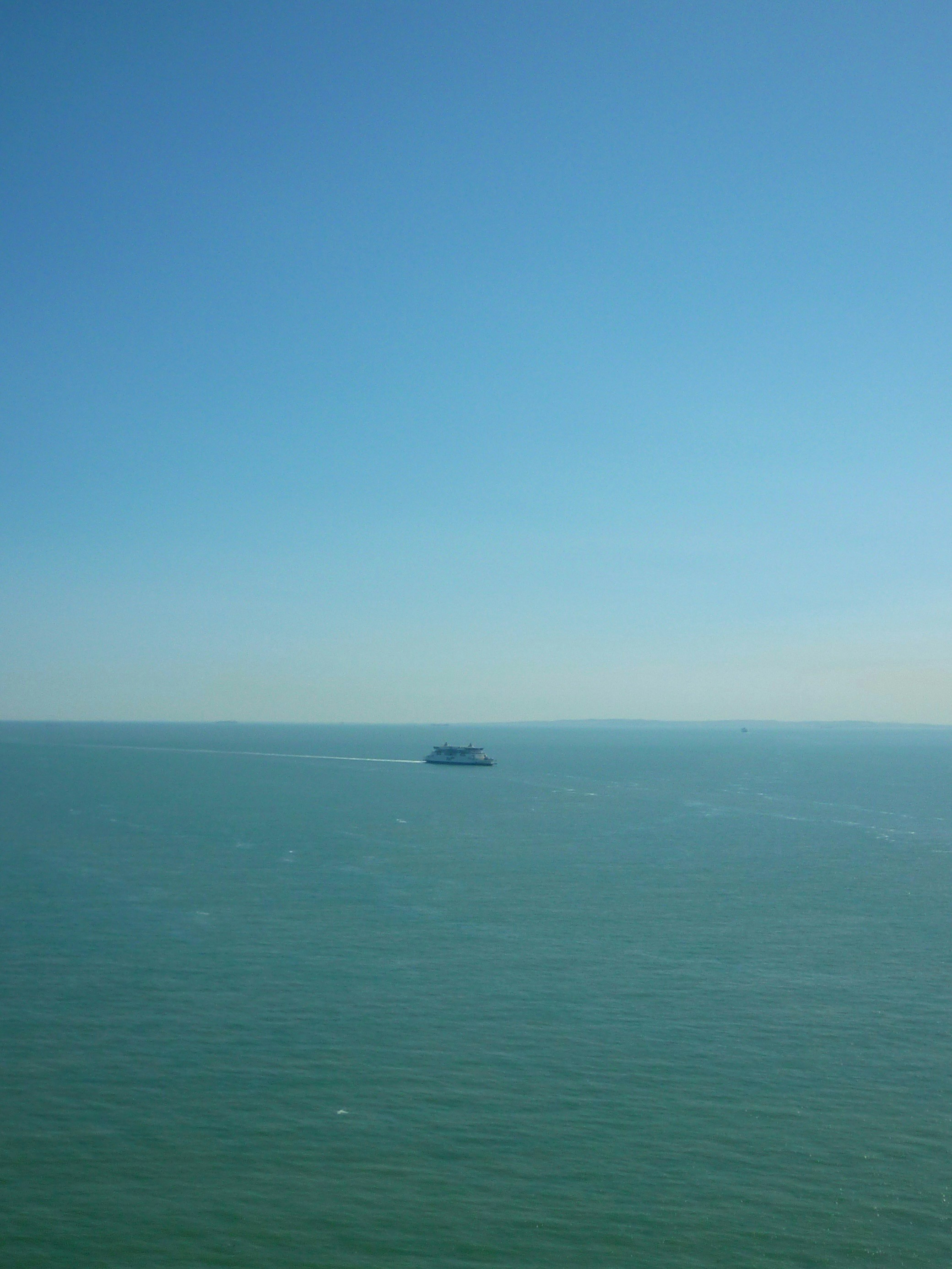 A lone ferry navigates through calm turquoise waters under a clear blue sky, evoking a sense of tranquility and adventure.