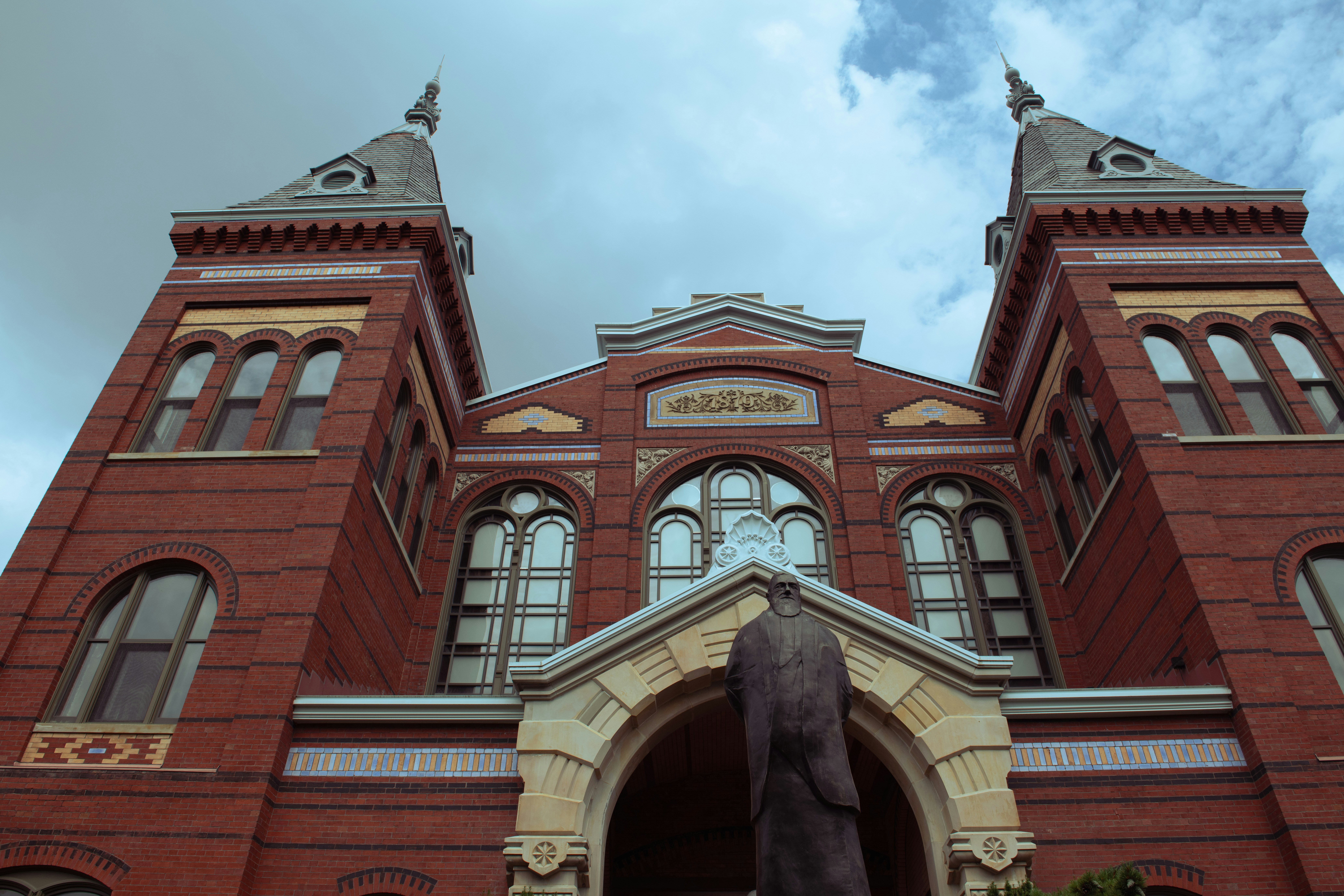 Historic brick building with twin towers and a prominent statue at the entrance, showcasing architectural grandeur.