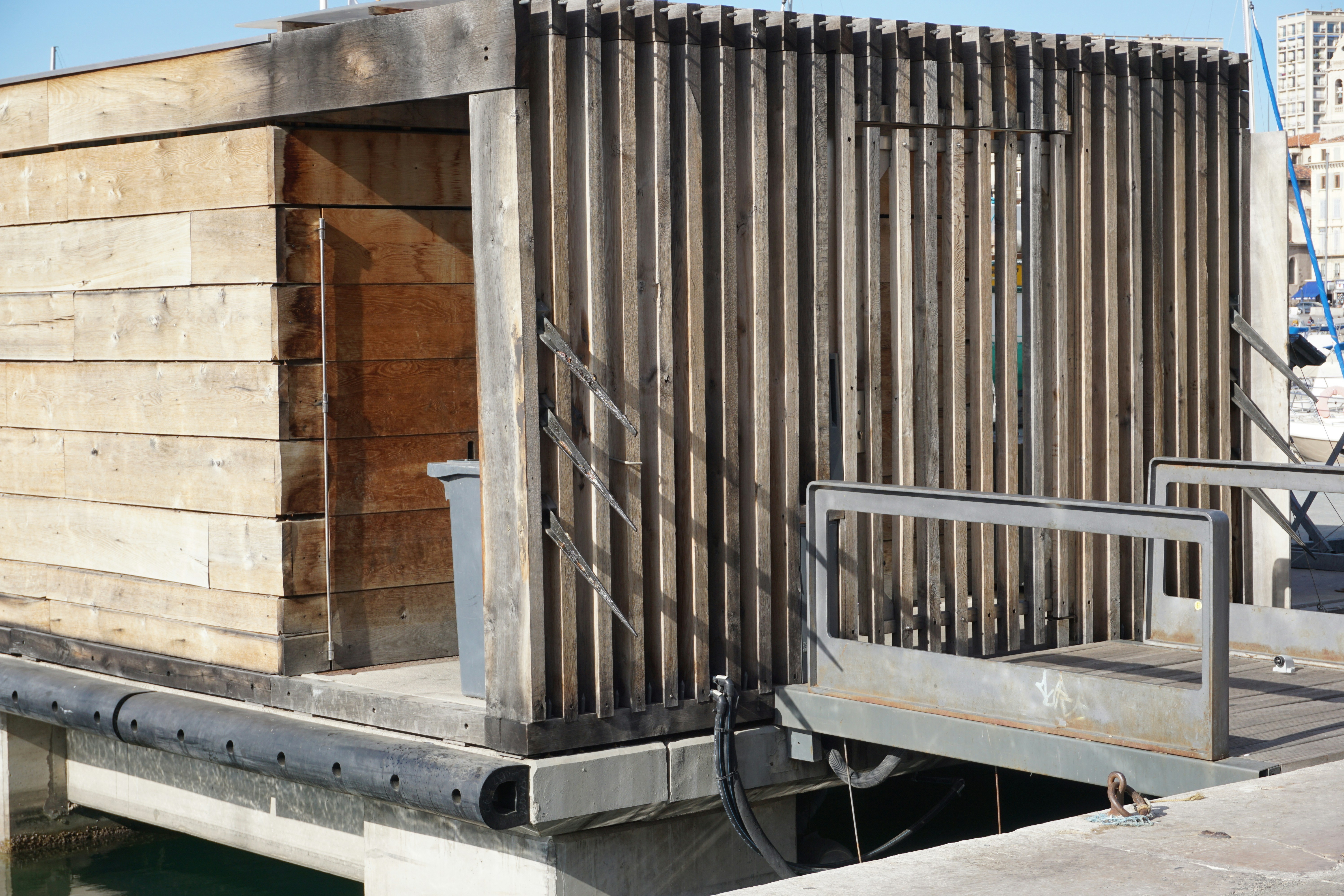 Contemporary wooden building with vertical slats, situated on a dock, showcasing a minimalist design. The structure emphasizes a harmonious relationship with its surroundings.