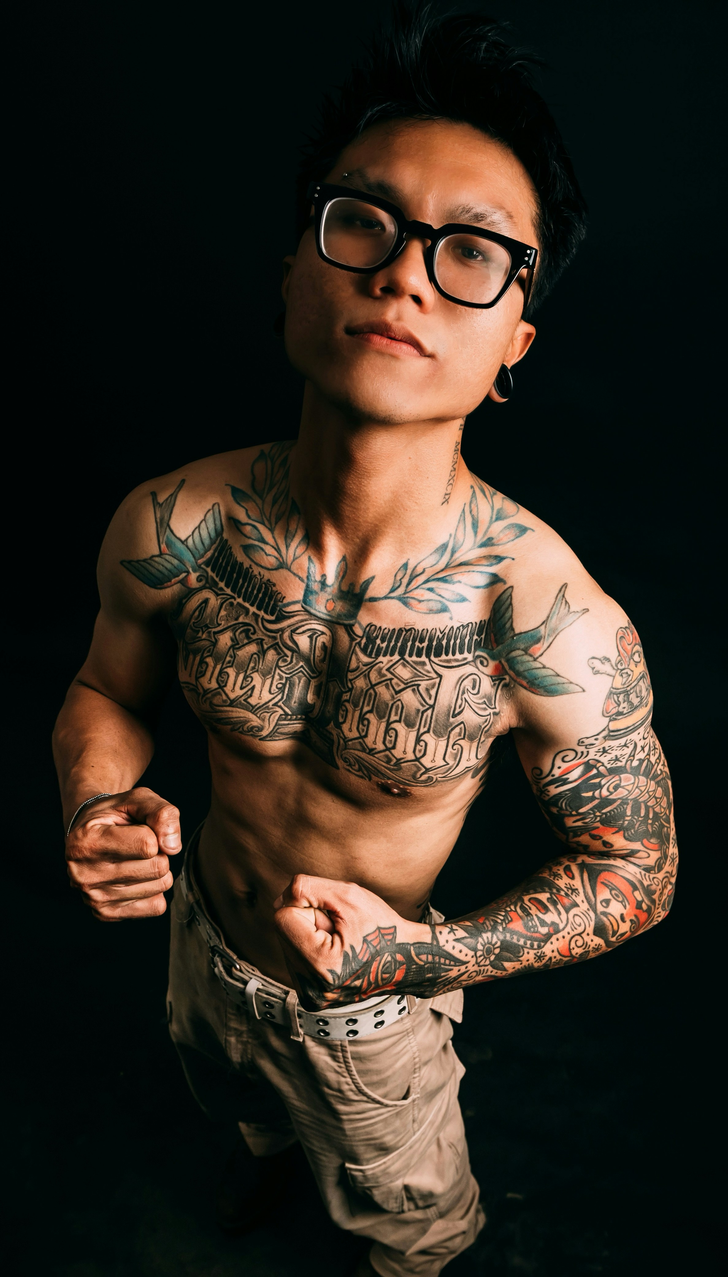 Muscular individual showcasing an array of intricate tattoos, posing confidently against a dark backdrop.