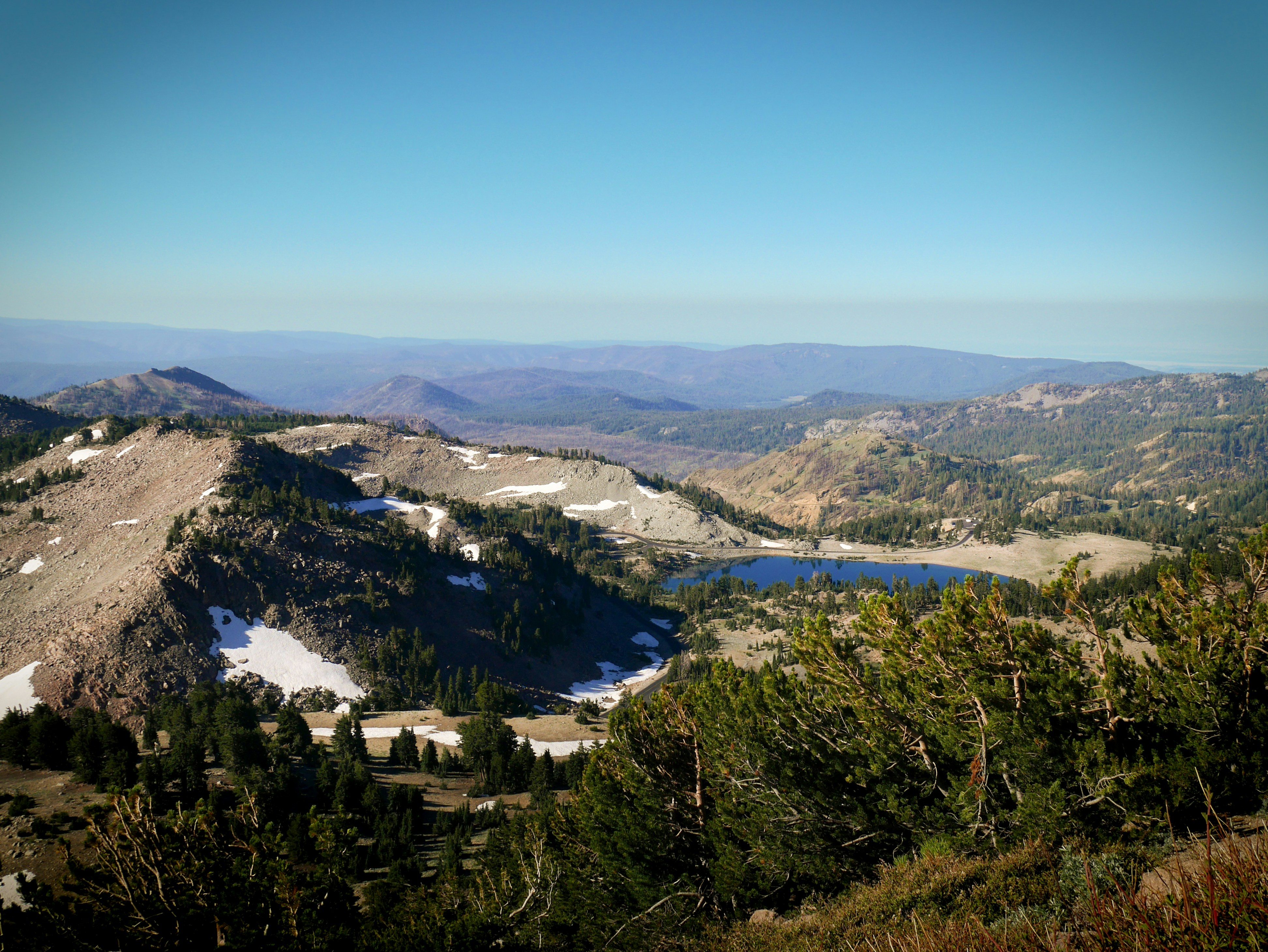 Mountain landscape with a lake and scattered snow patches.