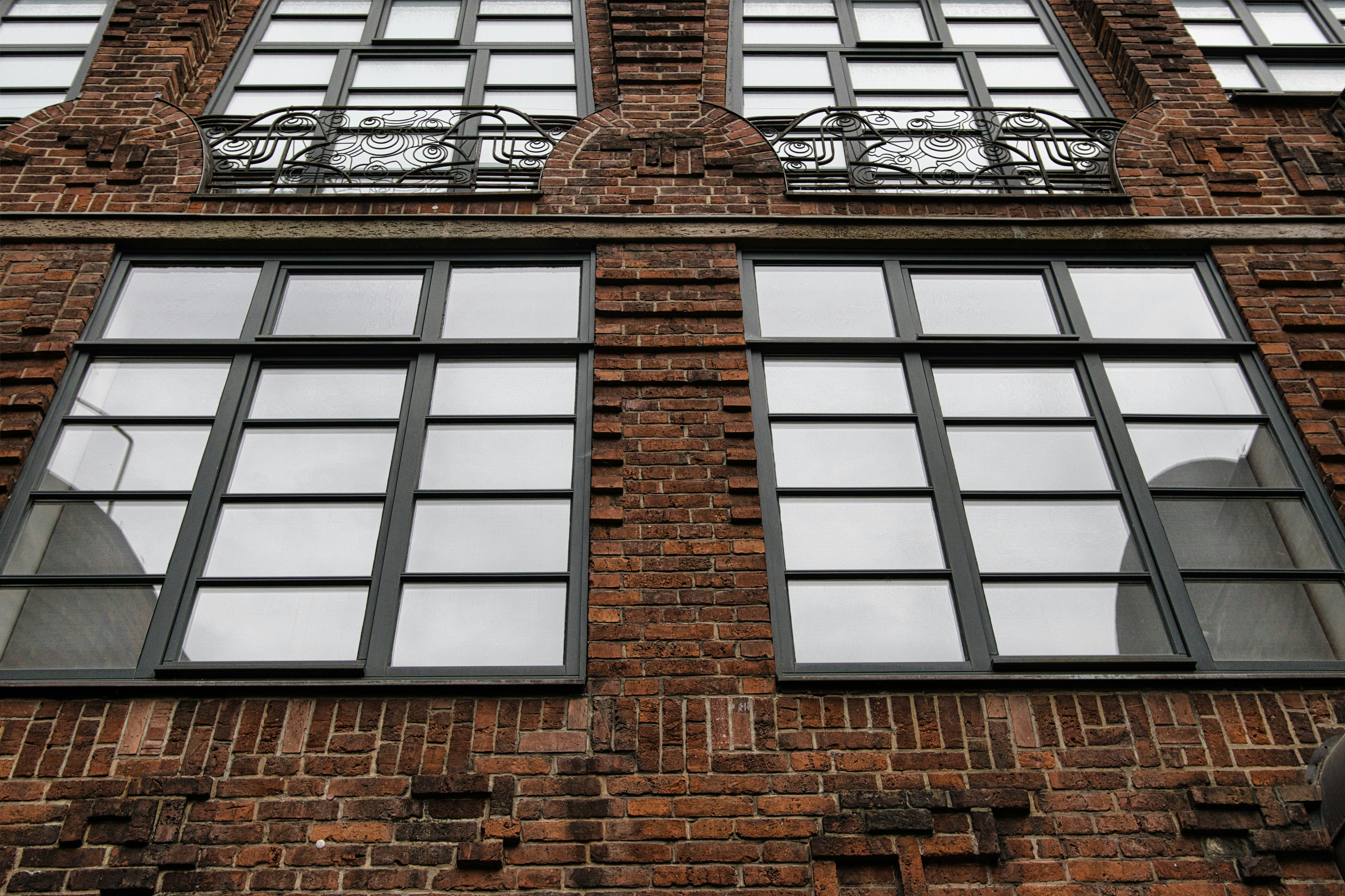 Symmetrical arrangement of large windows against a textured brick wall, highlighting architectural details and reflections.