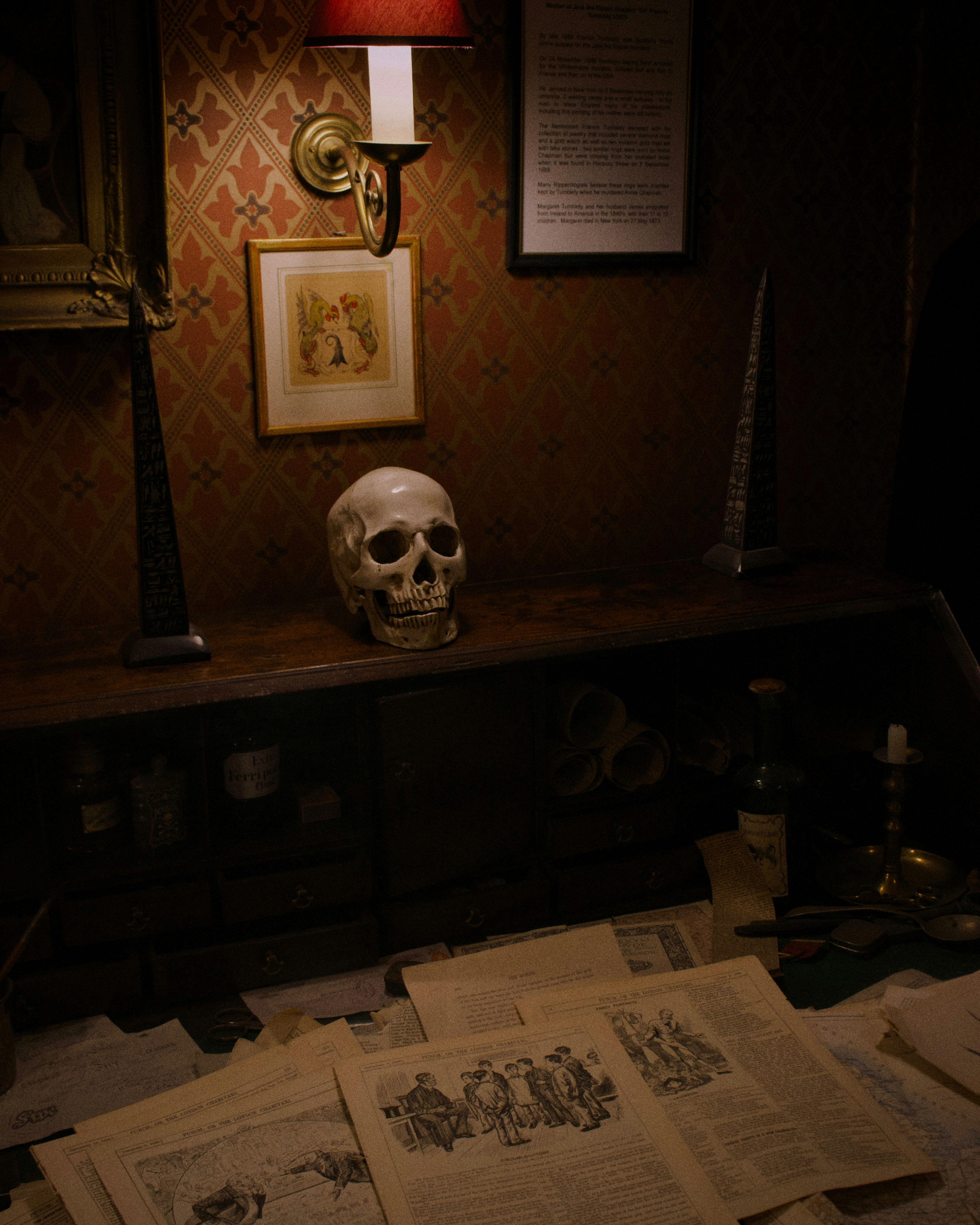 A skull sits on a desk with papers and lamp.