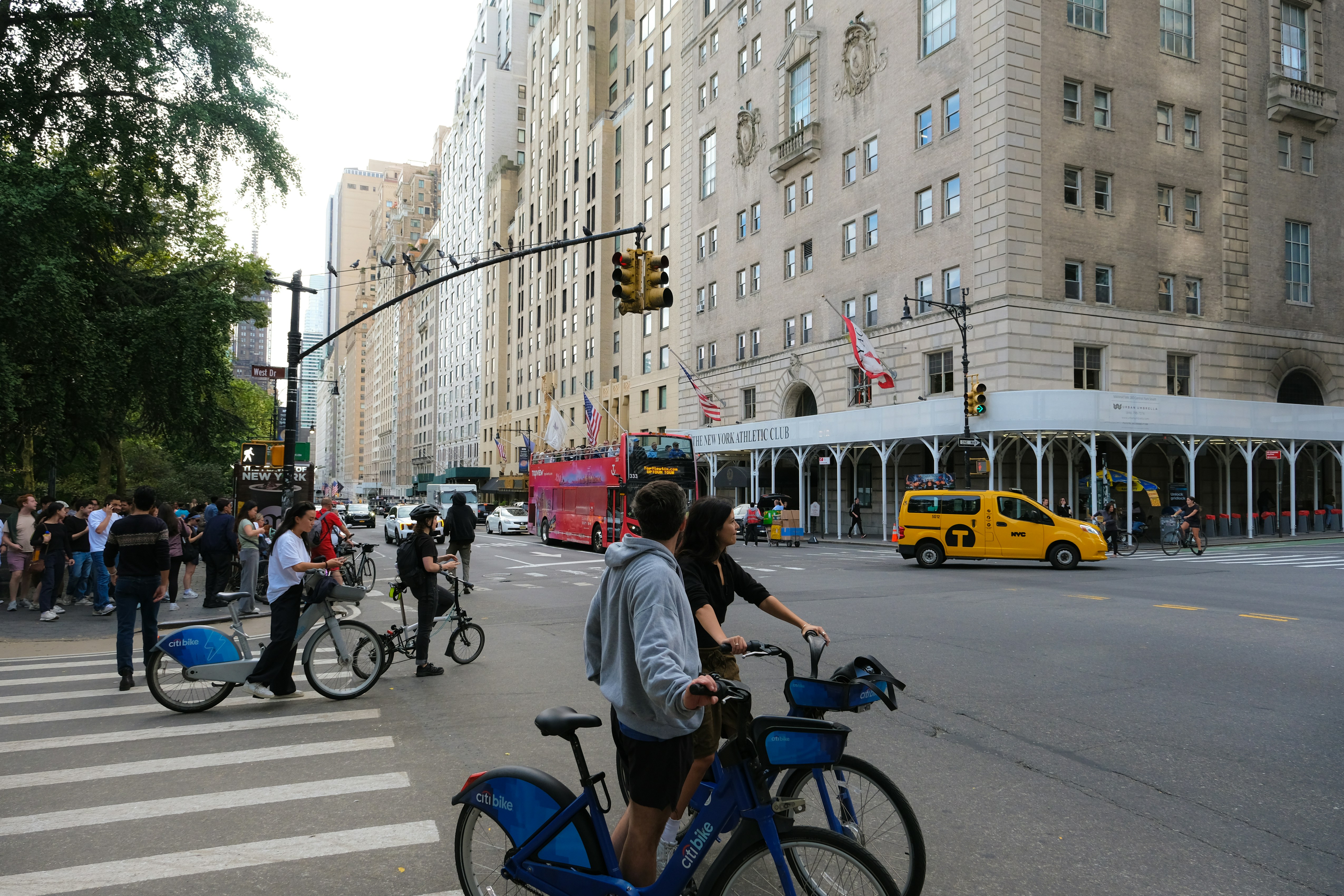 Busy city intersection filled with pedestrians and cyclists, showcasing urban life against a backdrop of towering buildings.