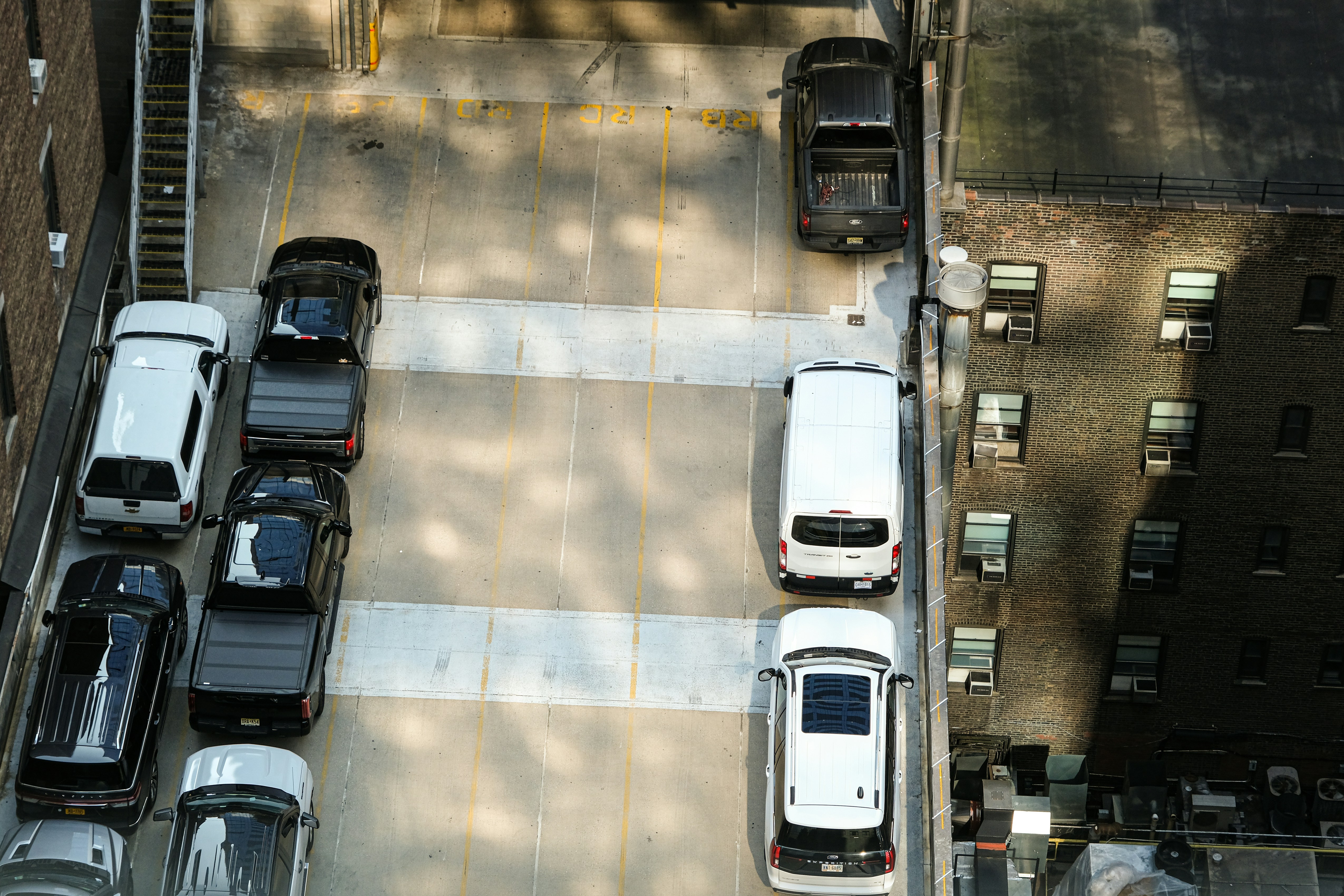 Aerial view of a structured parking lot showcasing various vehicles parked in designated spaces. The scene highlights urban design and vehicle arrangement.